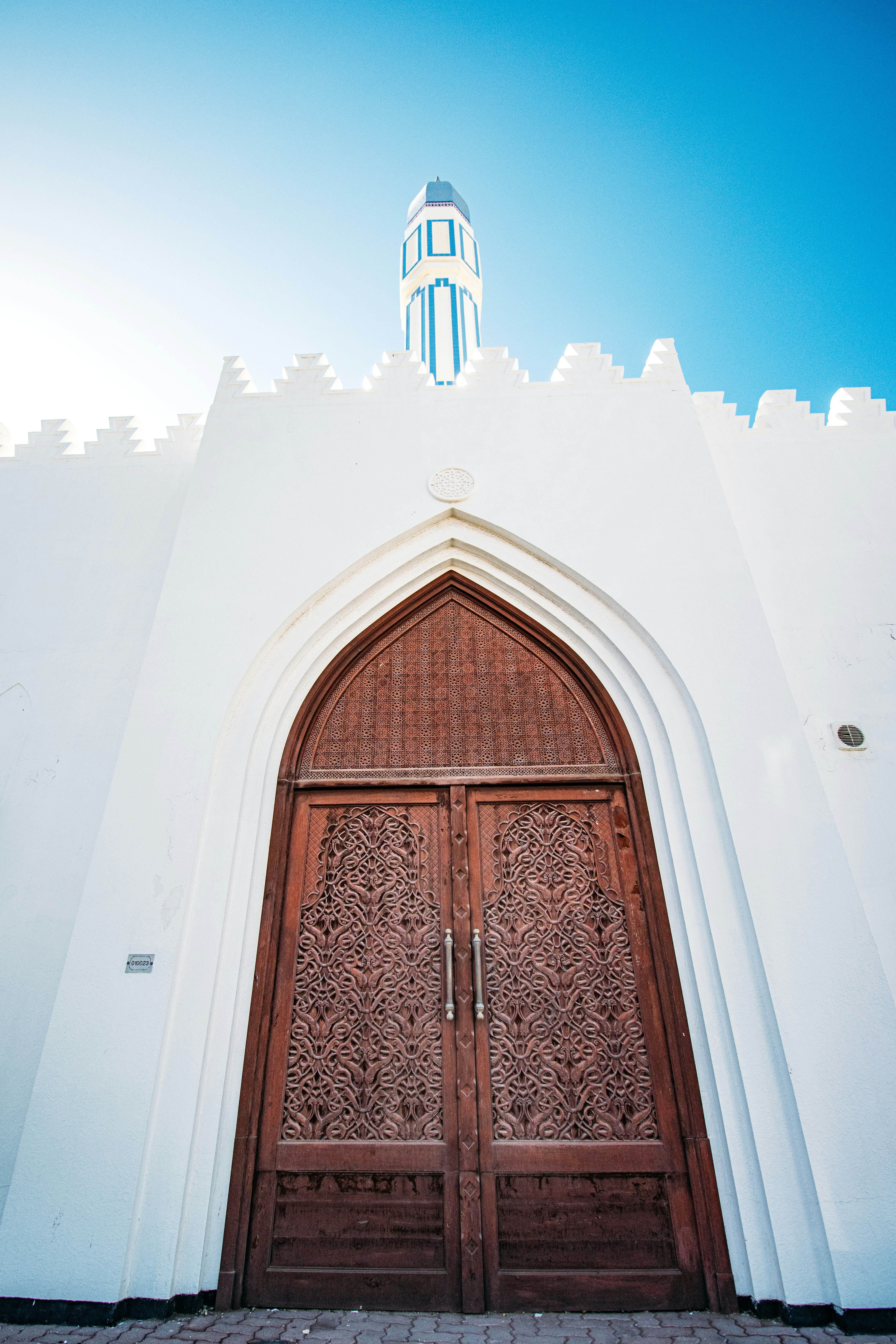 White Fortress Arch with Carved Wooden Doors Against a Bright Blue Sky