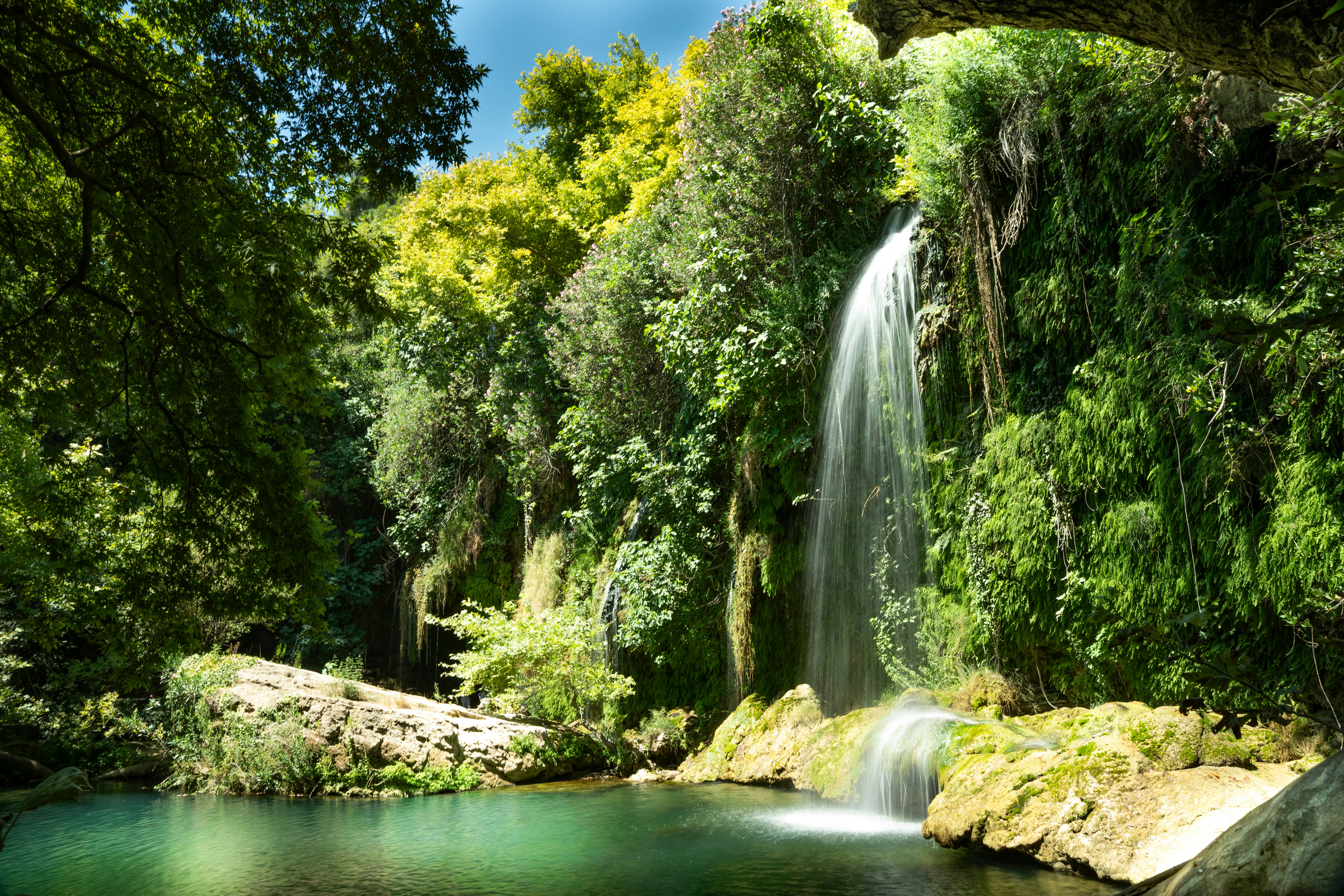 Emerald Cascade: Sunlit Falls Between Forested Cliffs