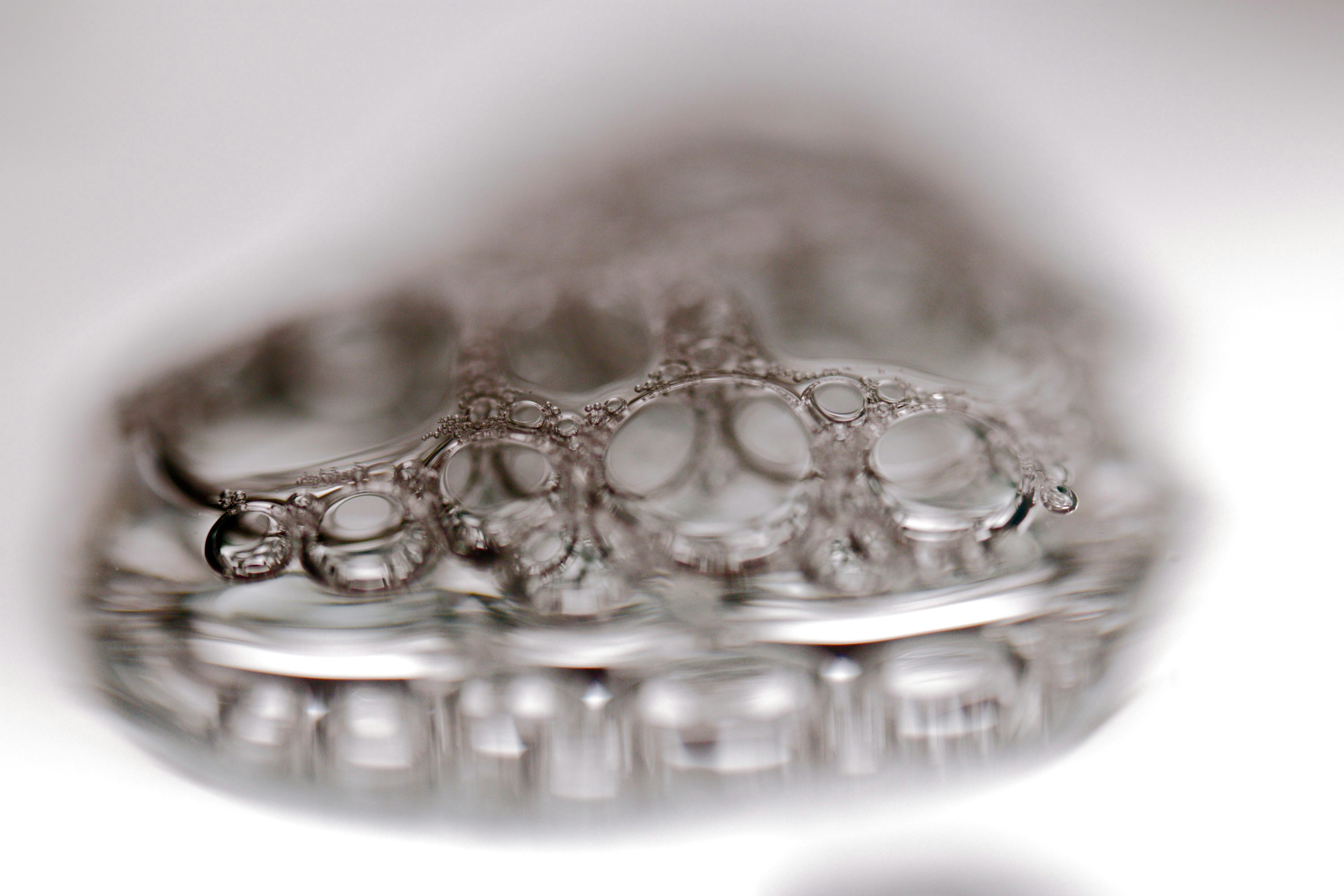 Close-up of soap bubbles forming a delicate lattice on a reflective surface, with soft, diffuse lighting and a shallow depth of field. A tactile macro study emphasizing texture and transparency.