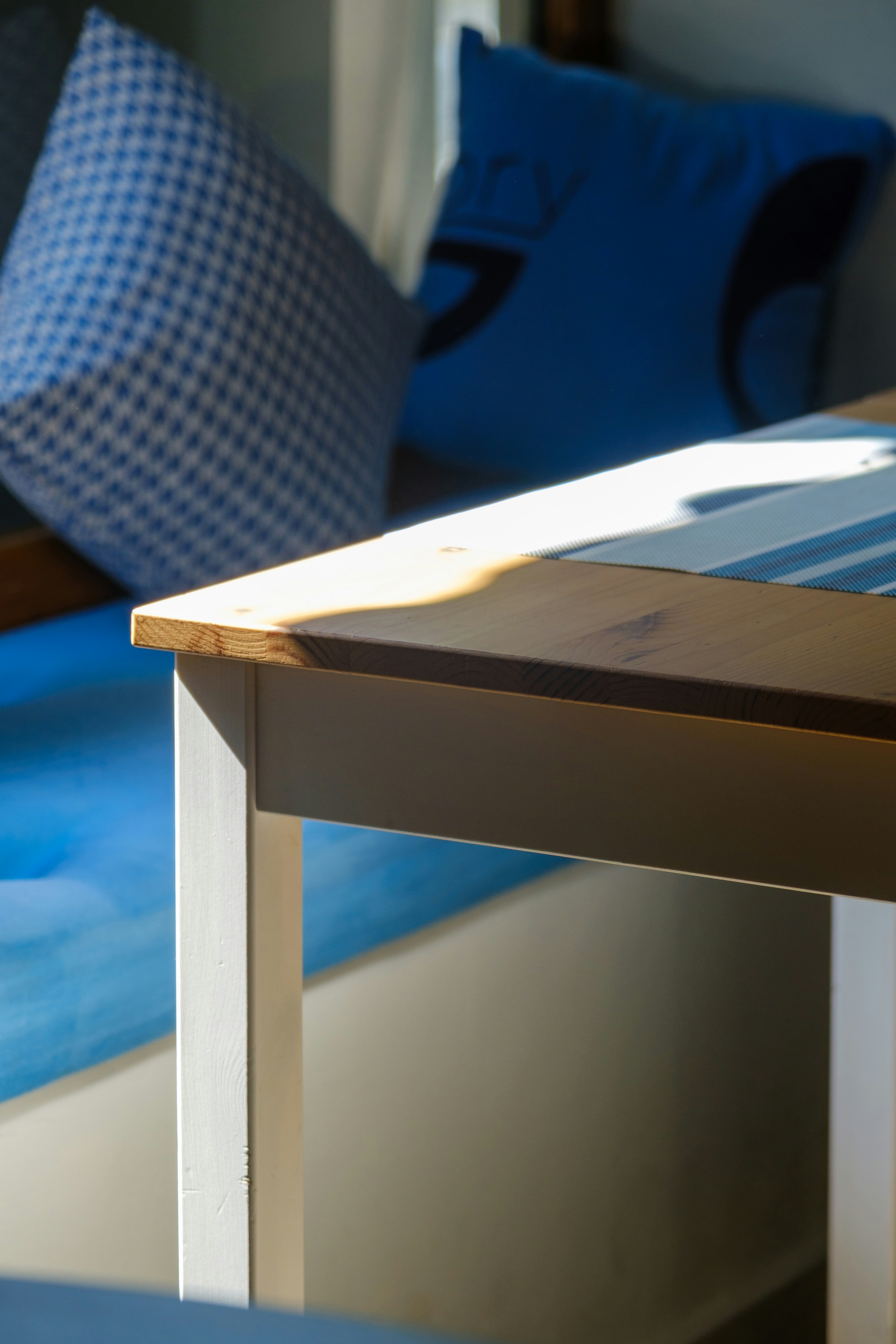 Sunlit Edge: A Wooden Table in Focus Against Cozy Cushions