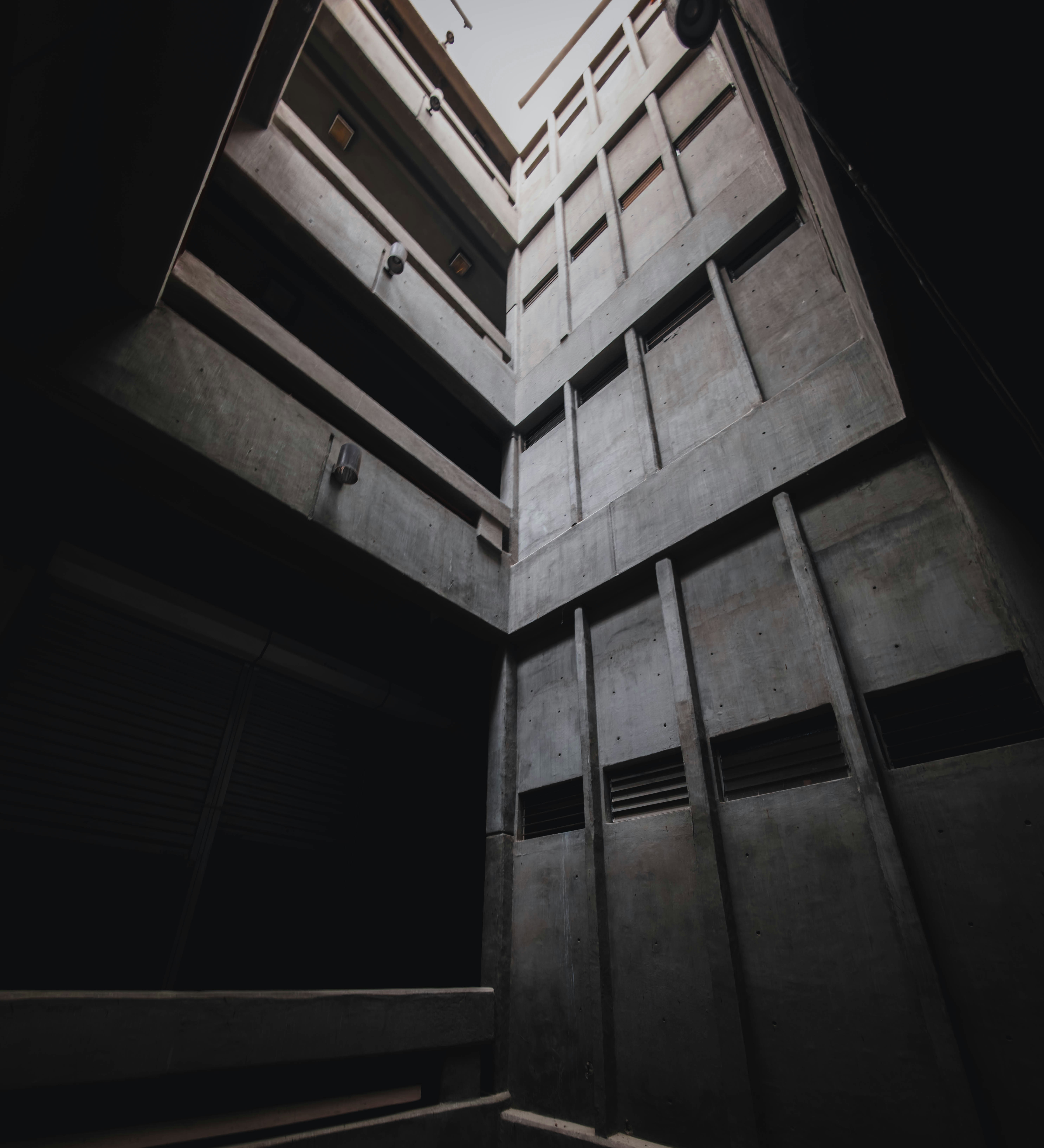 Industrial concrete atrium opens to a pale sky, with angular walls and sharp lines creating a dramatic vertical perspective.