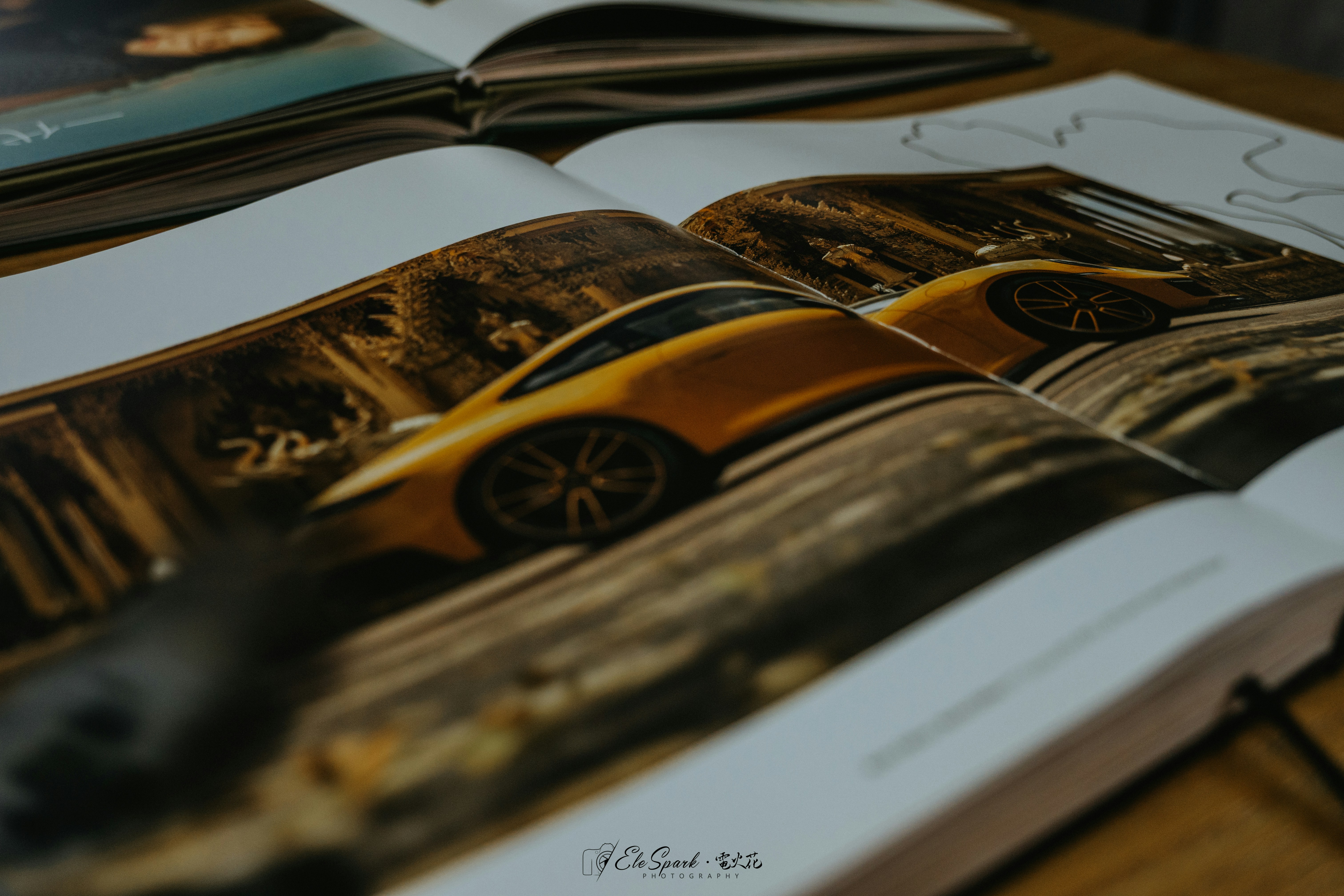 Close-up of glossy magazine pages featuring a yellow sports car; shallow depth of field and warm tones emphasize the vehicle image while blurred surrounding pages provide context.