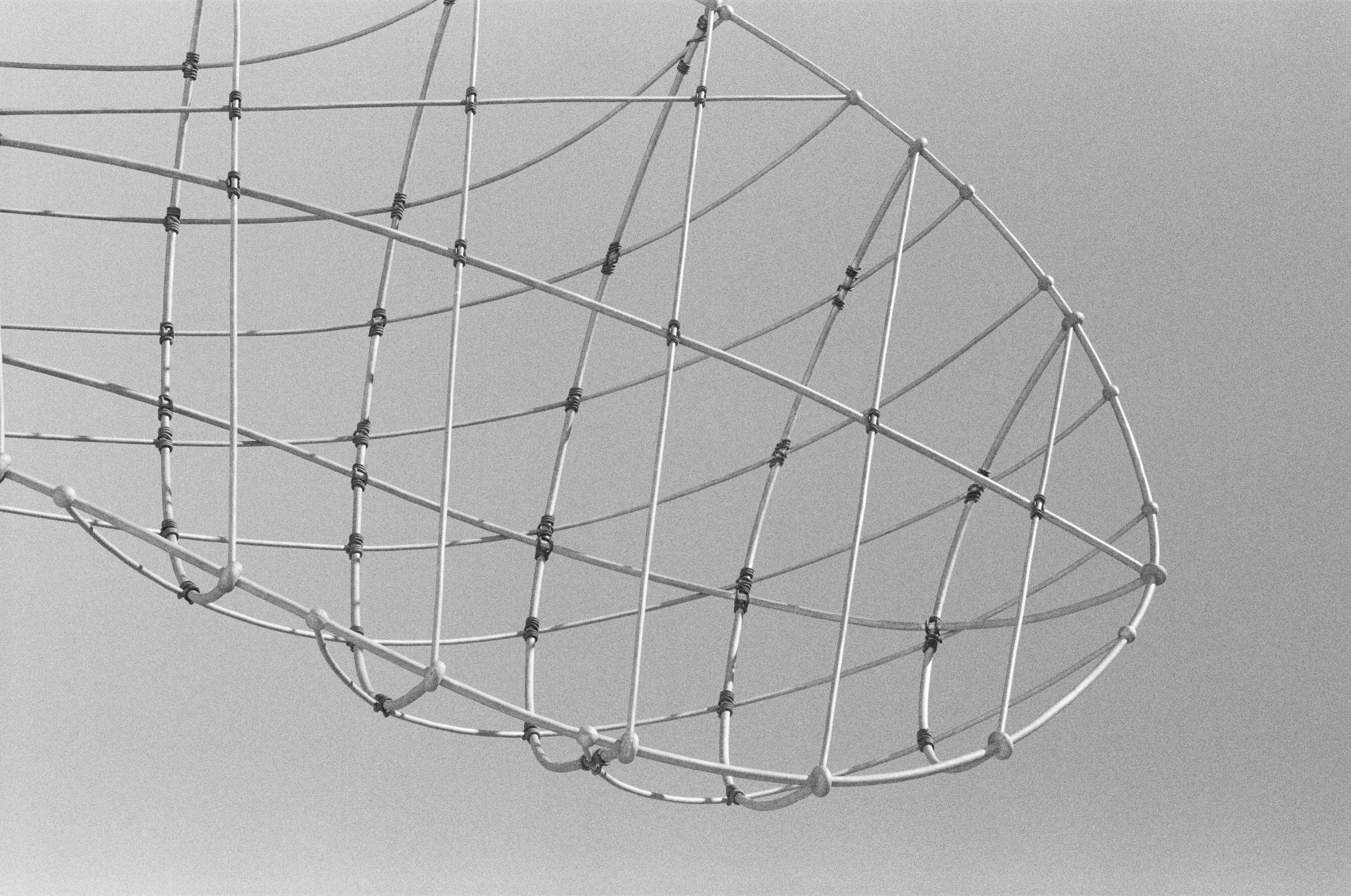 A close-up of a curved parabolic antenna lattice against a pale sky, highlighting the metallic gridwork as the focal subject.
