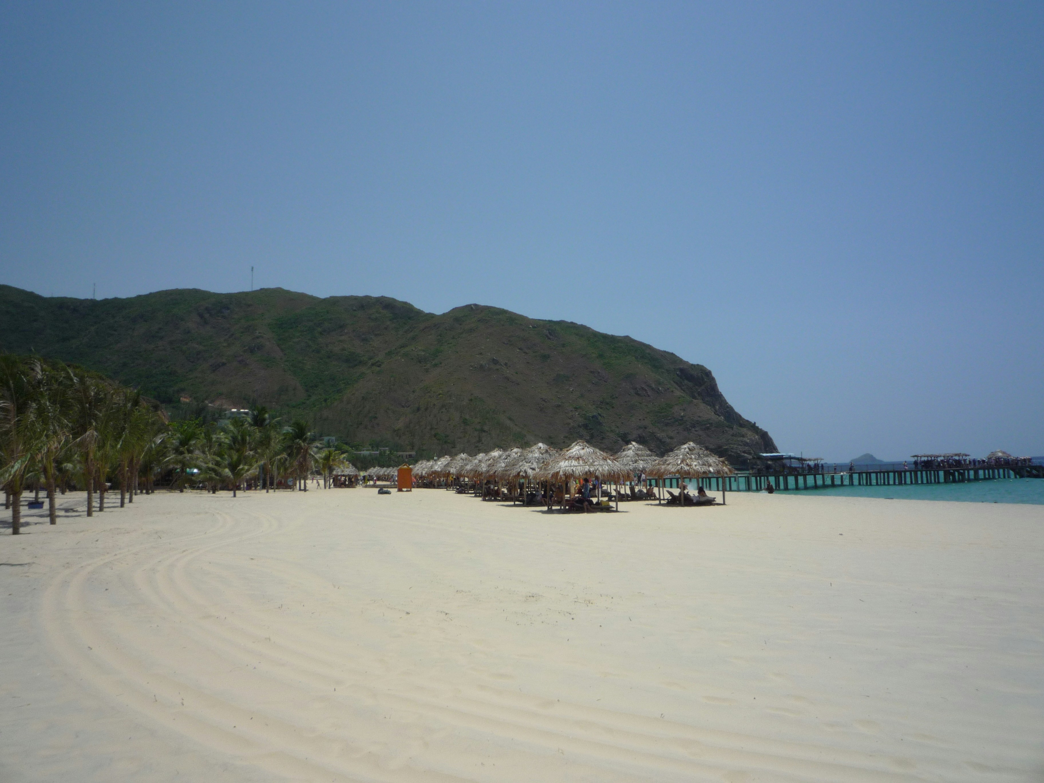 Sunlit Beachscape with Thatched Palapas and Distant Hills