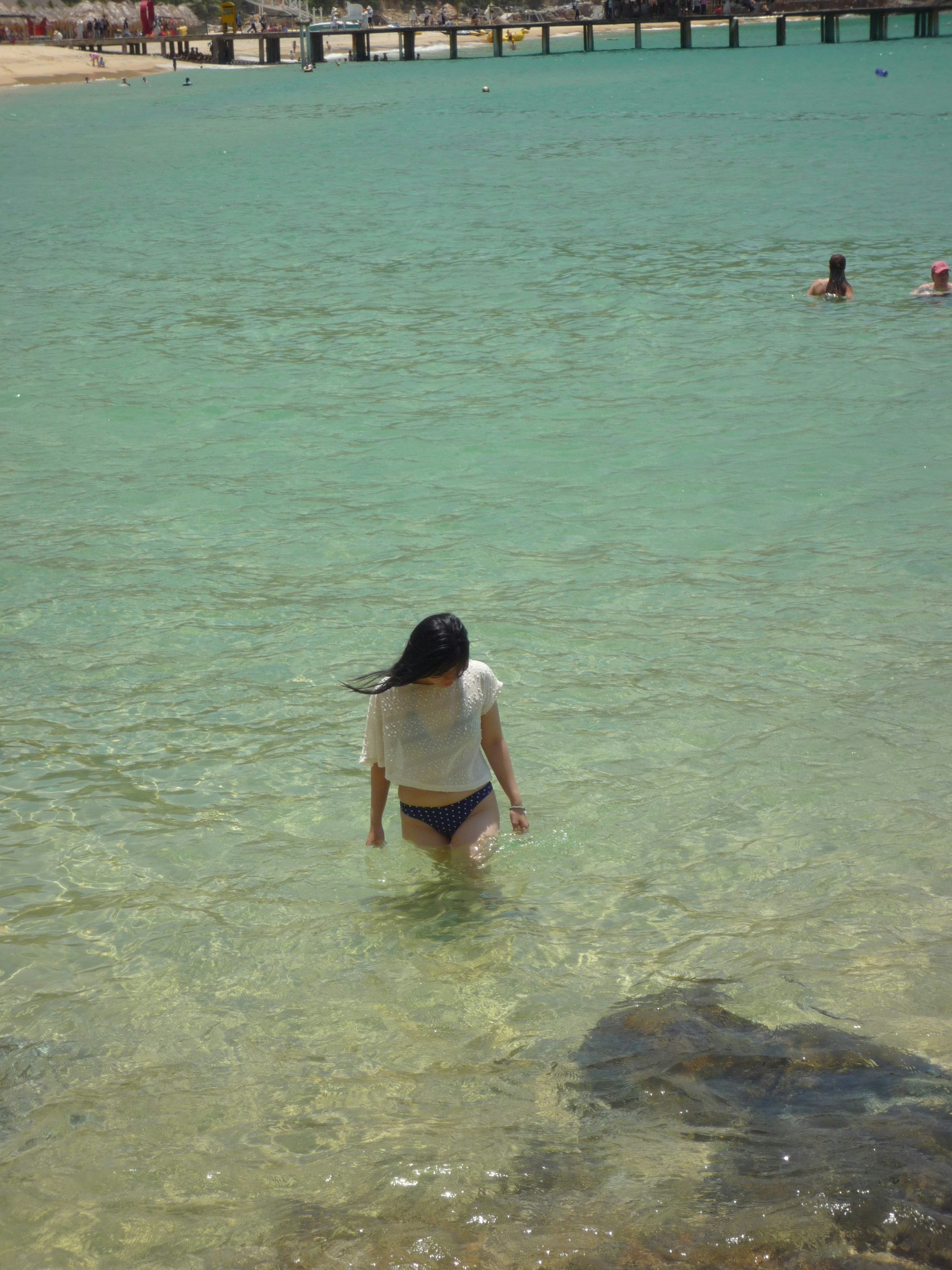 Girl in turquoise sea stepping toward shore on a sunlit day