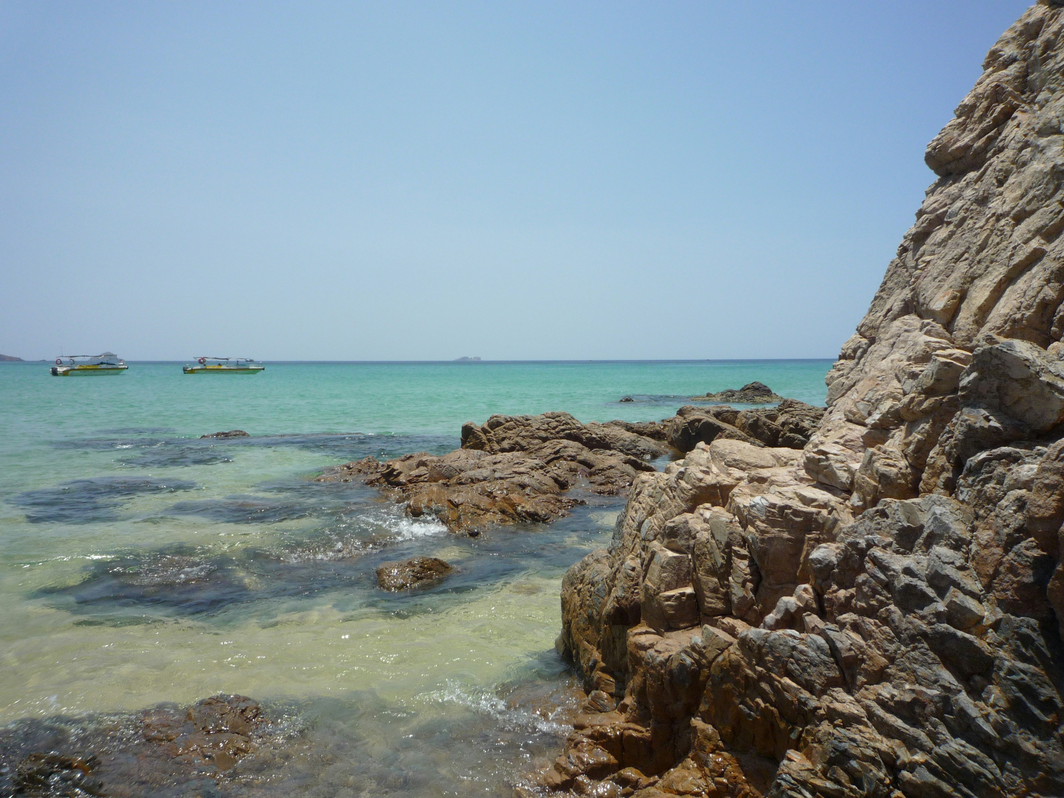 Sunlit Cove: Boats at the Quiet Edge of a Rocky Shore