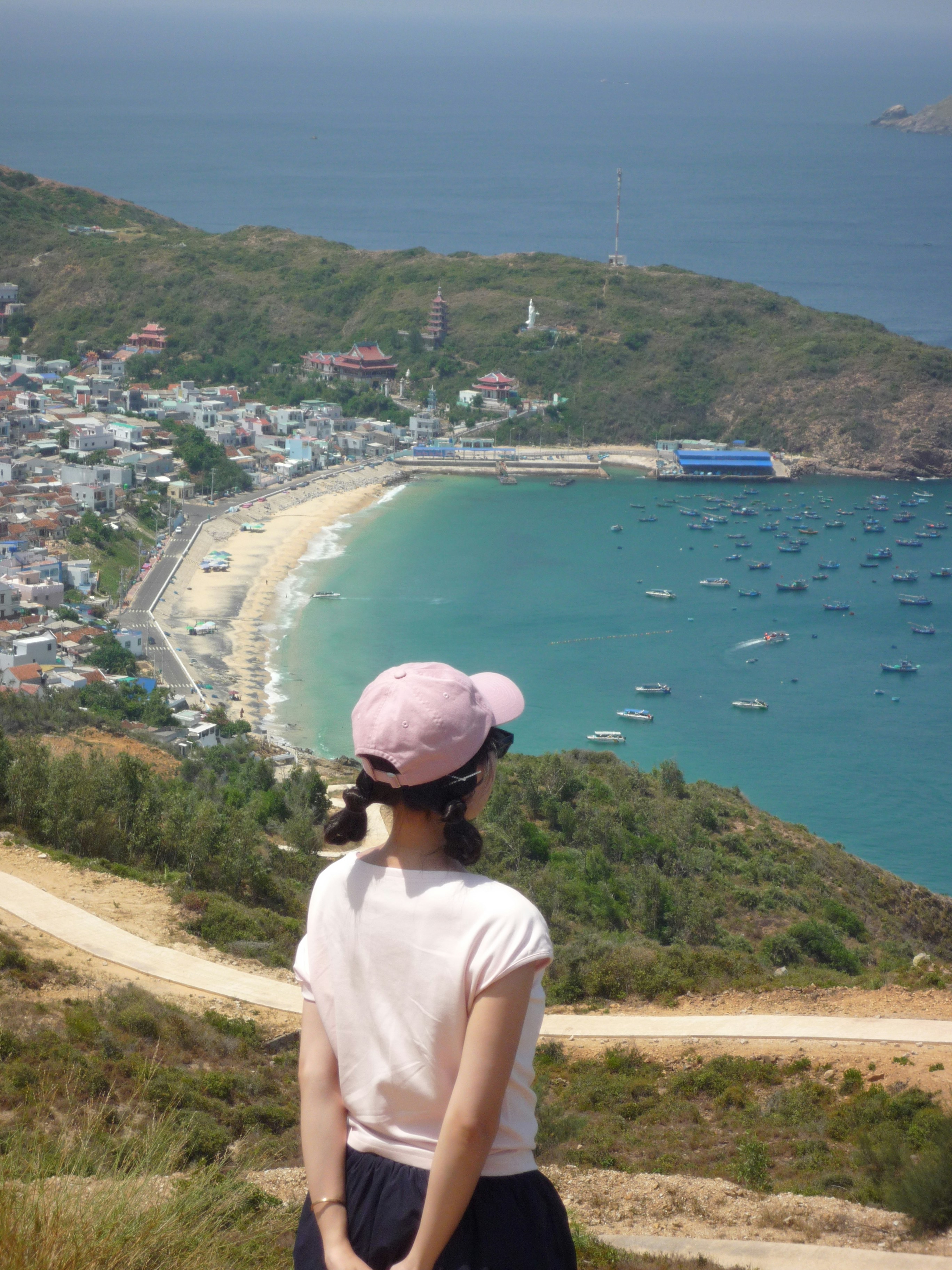 Girl overlooking a coastal town and turquoise bay from hillside viewpoint