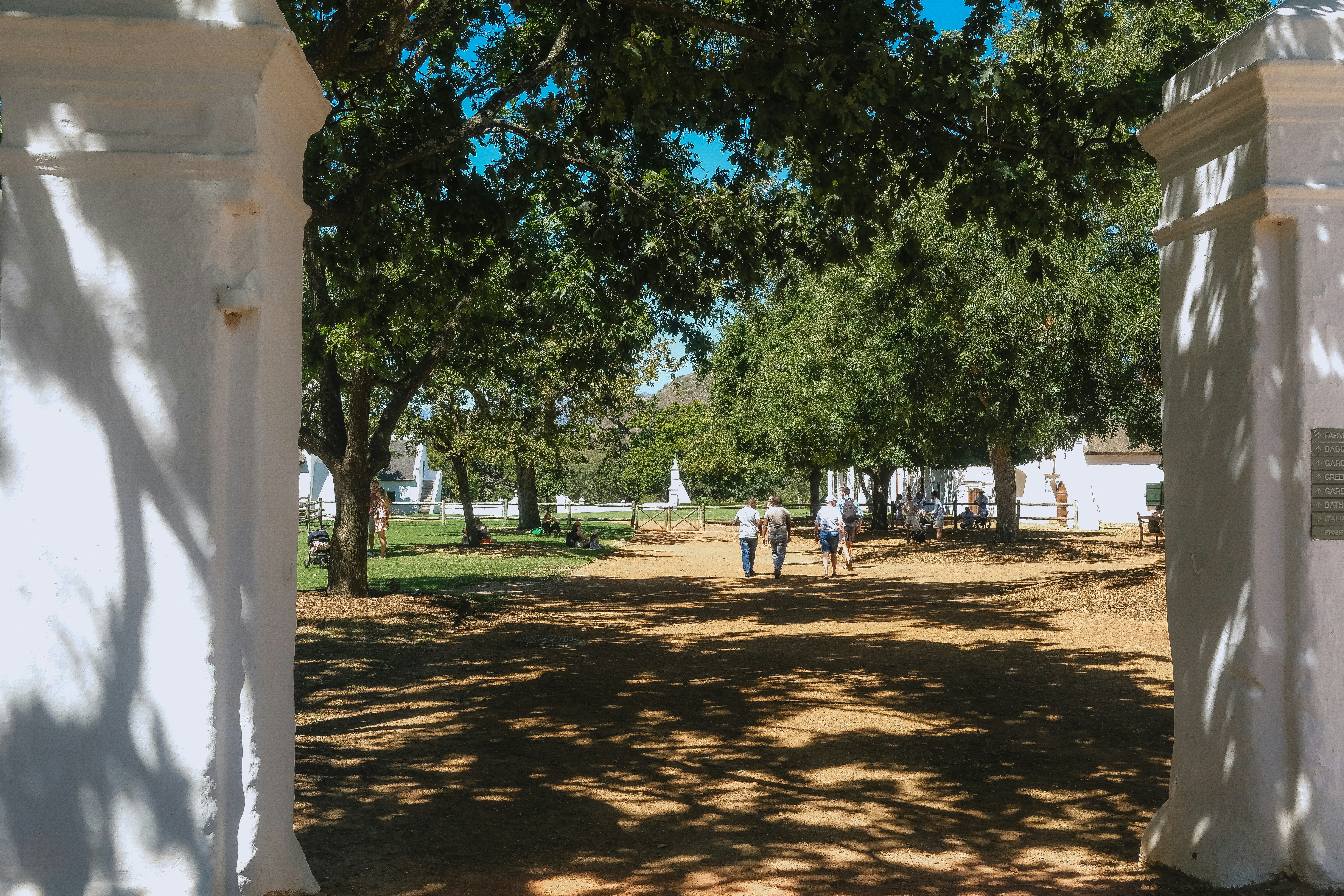 Path Through the Shade: Visitors Walk Toward the White Columns