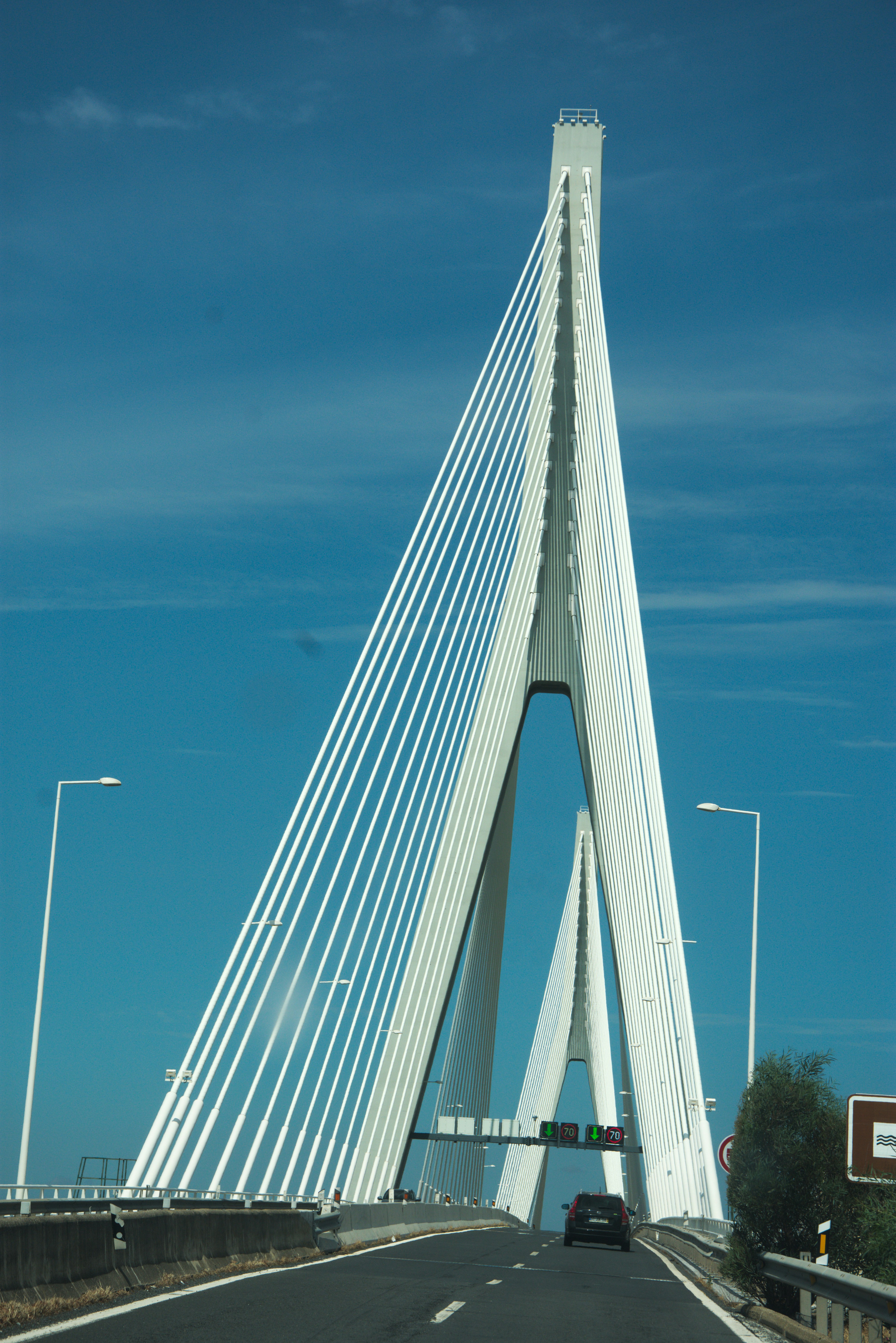 Cable-stayed tower rises over a two-lane highway under a clear blue sky