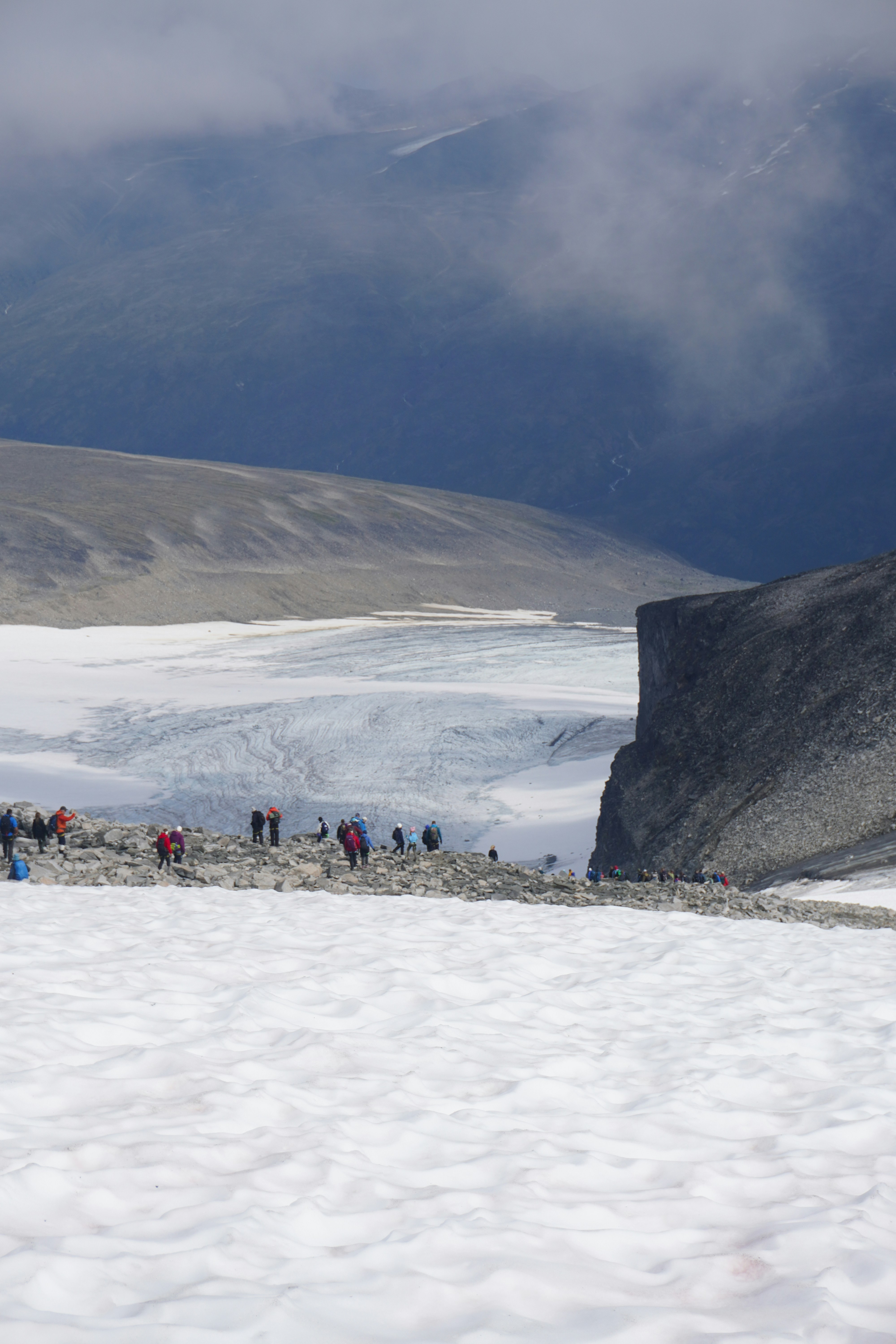 Hikers Traverse a Snowfield Beneath Smoke-Scarred Mountains