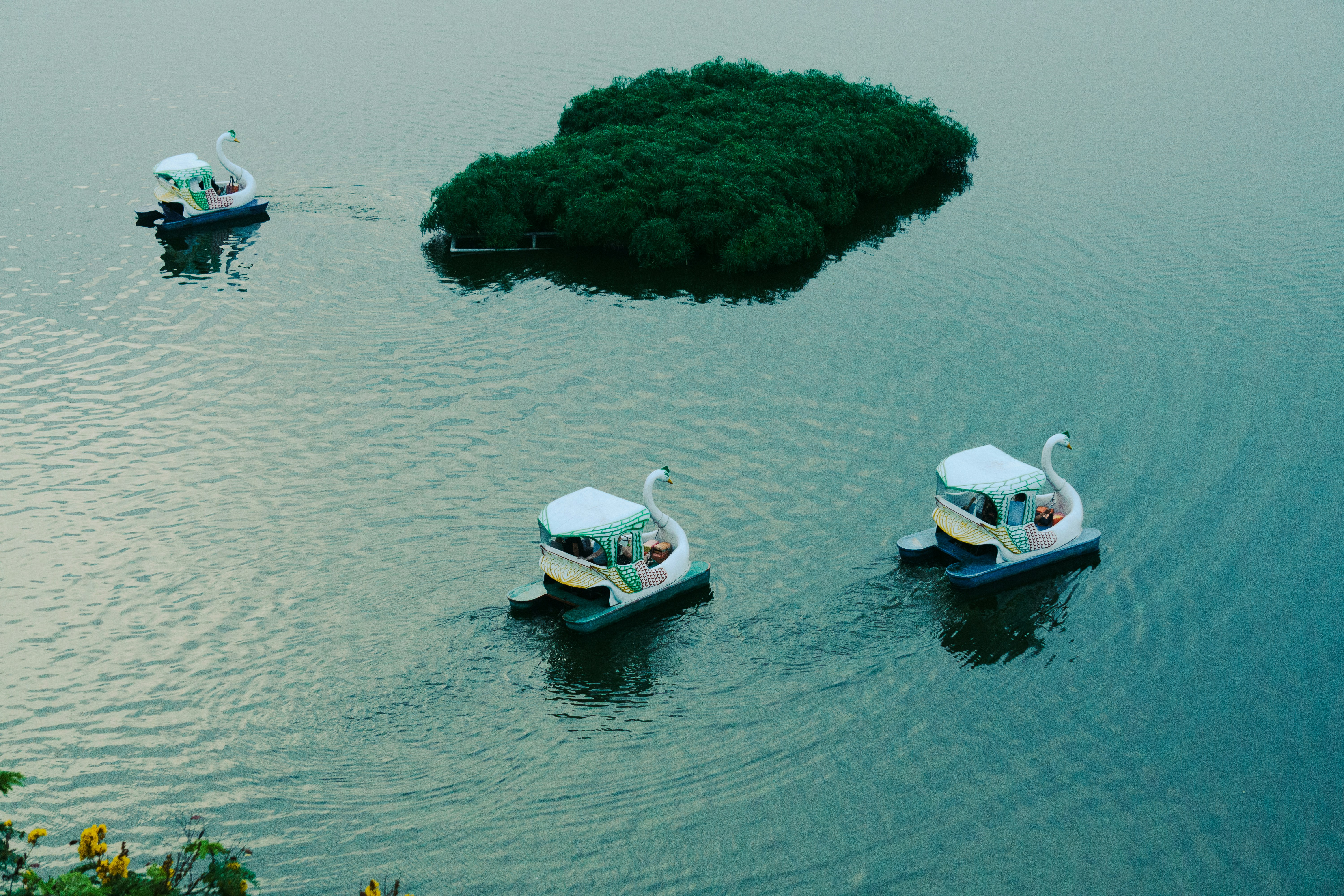 Three swan-ornamented boats drift over a tranquil turquoise lake