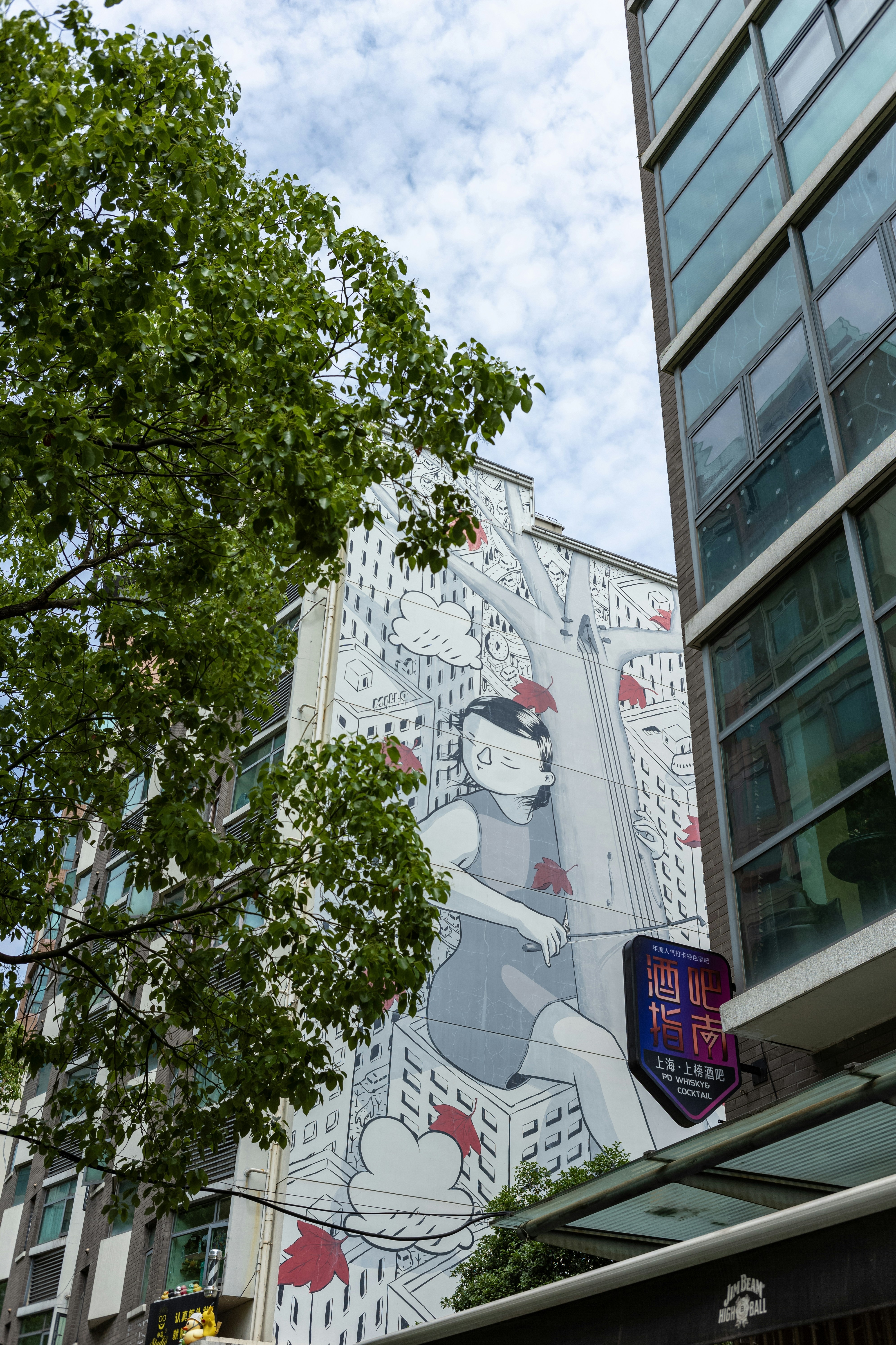 Urban mural on glassy high-rise wall framed by tree canopy
