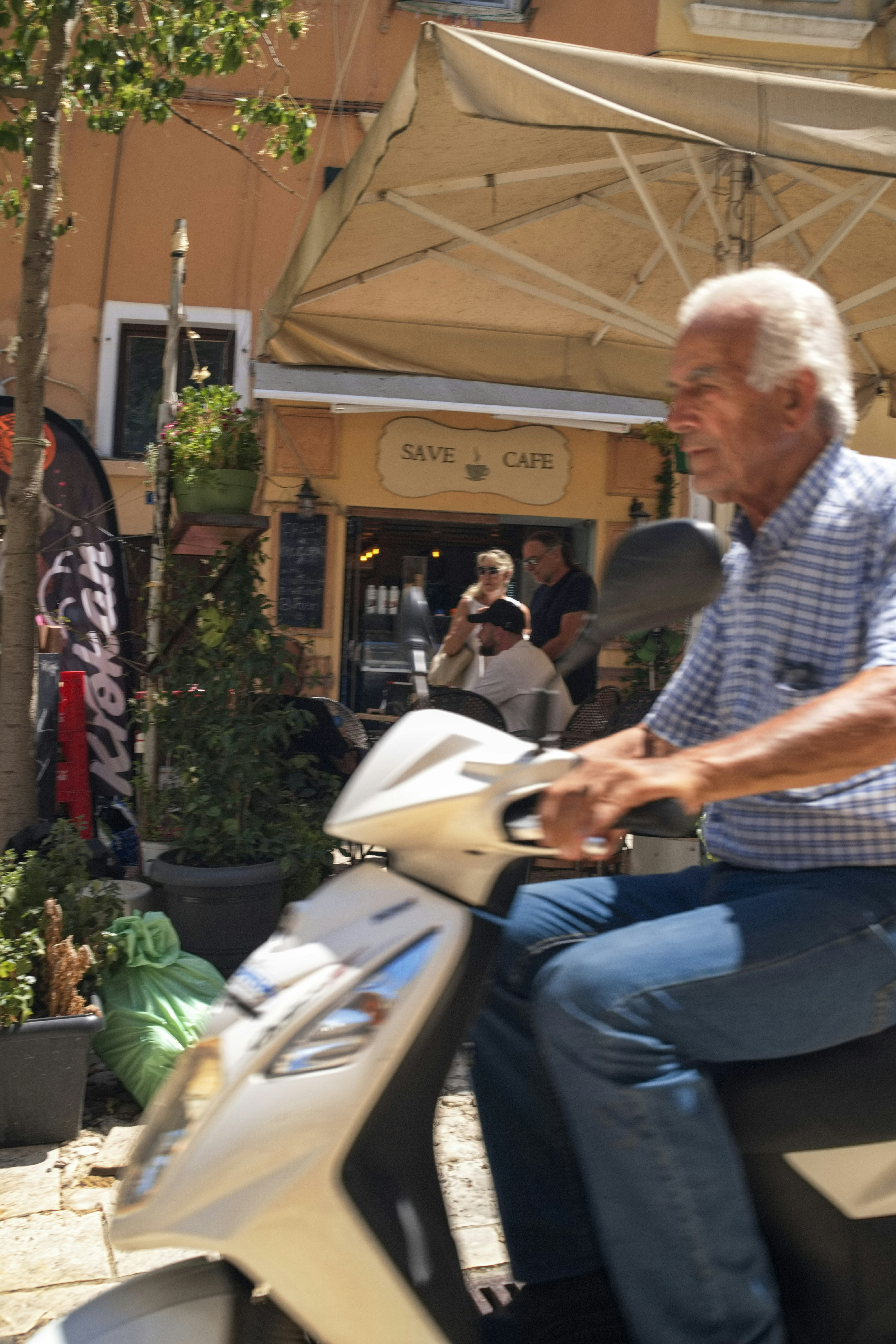 Scooter in Motion by a Sunlit Café