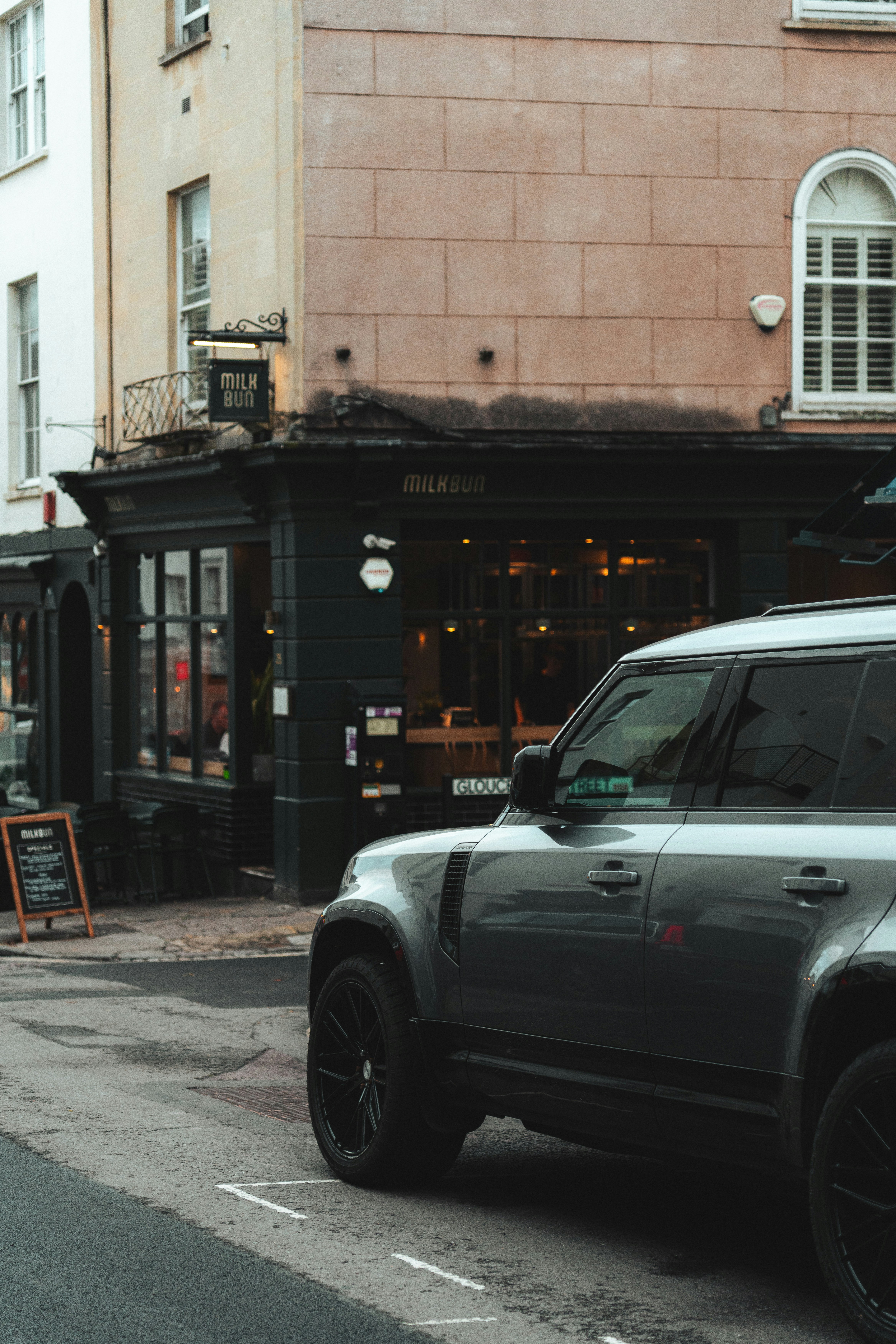 Industrial Street Presence: A Modern SUV Hangs at the Curb Before a Cafe Facade
