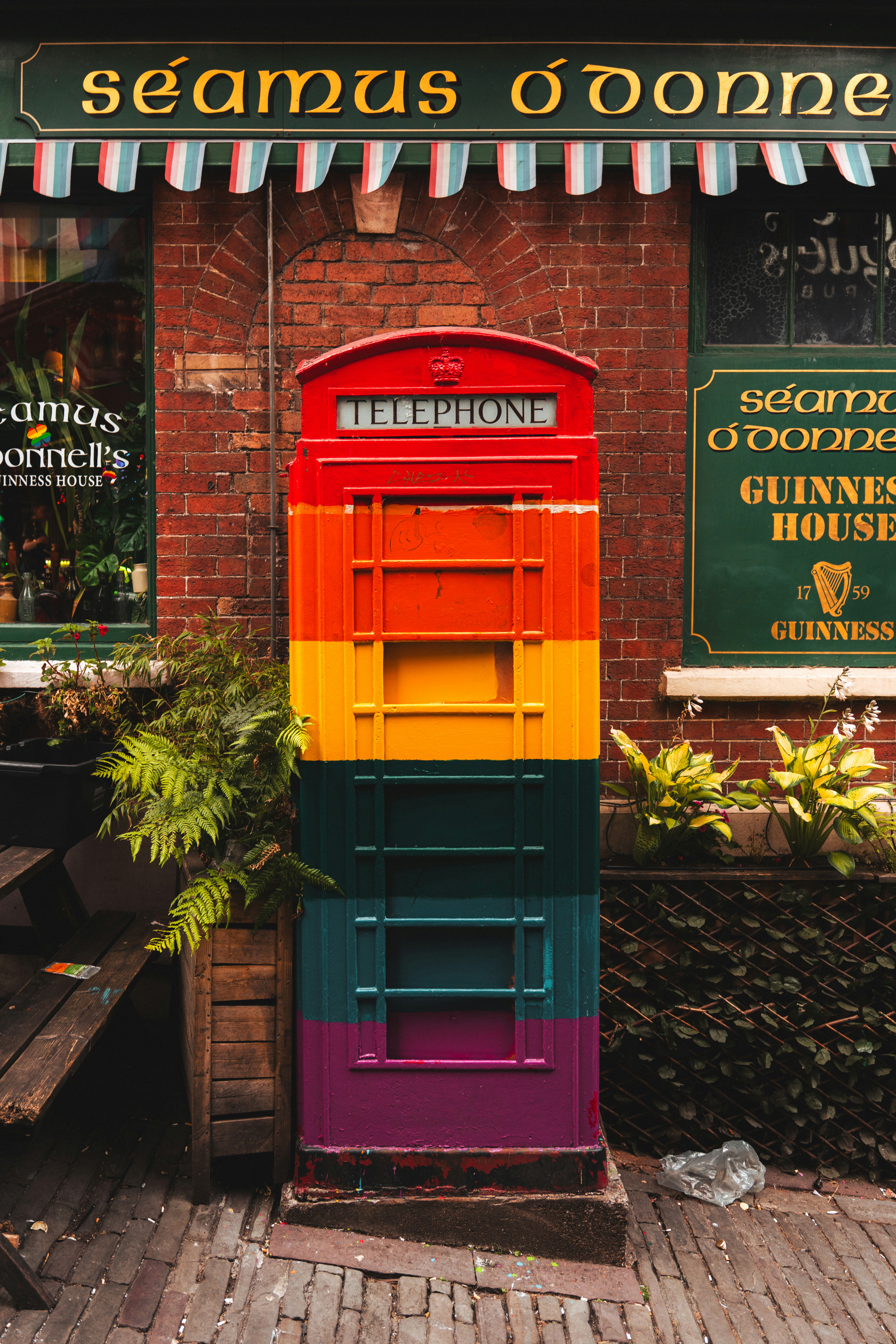 Rainbow Cabinet: A Colorful British Phone Booth Stands Between Greenery and Pub Signage