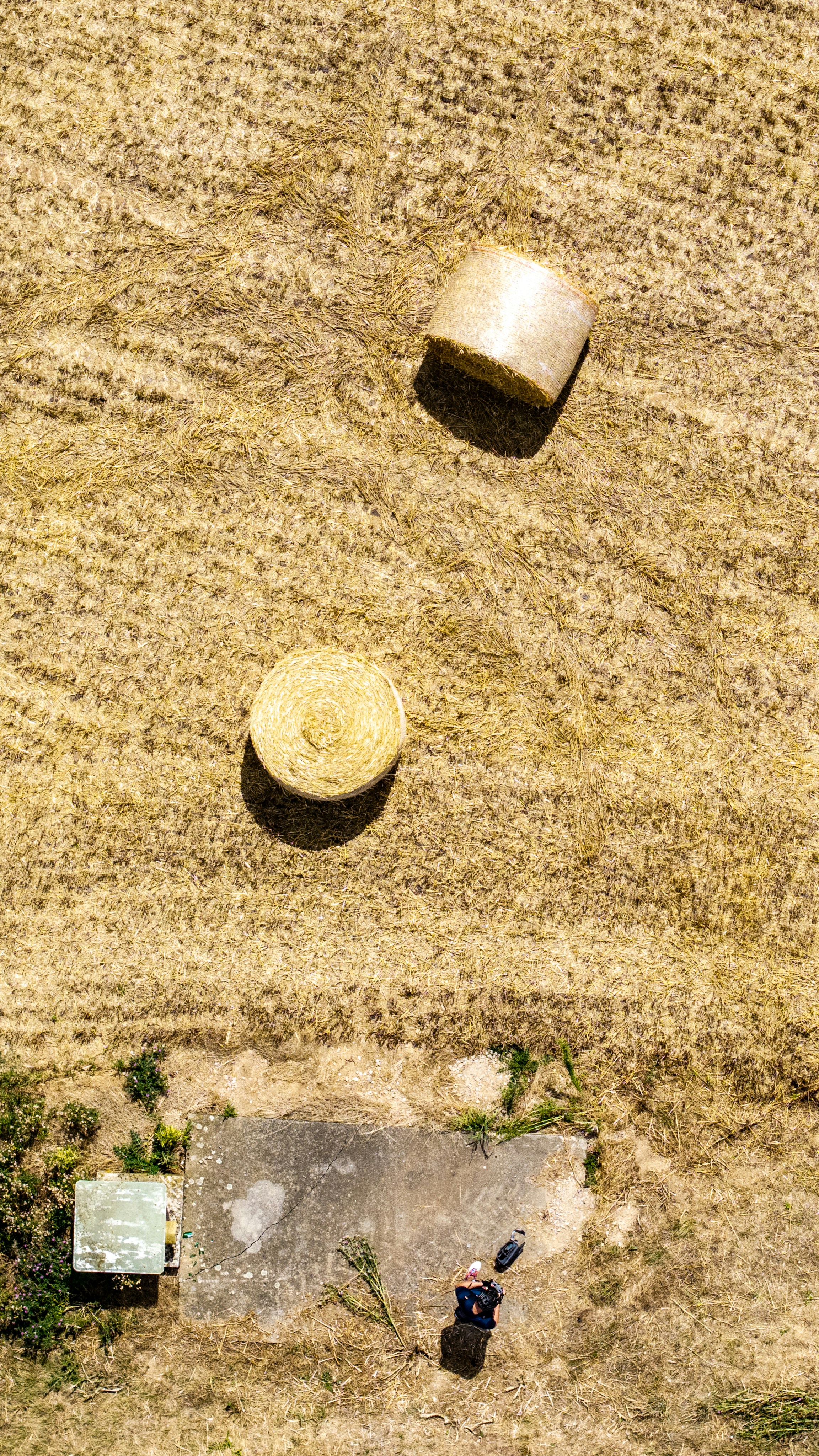 Aerial View: Circular Hay Bales and Ground Crew in Brown Field