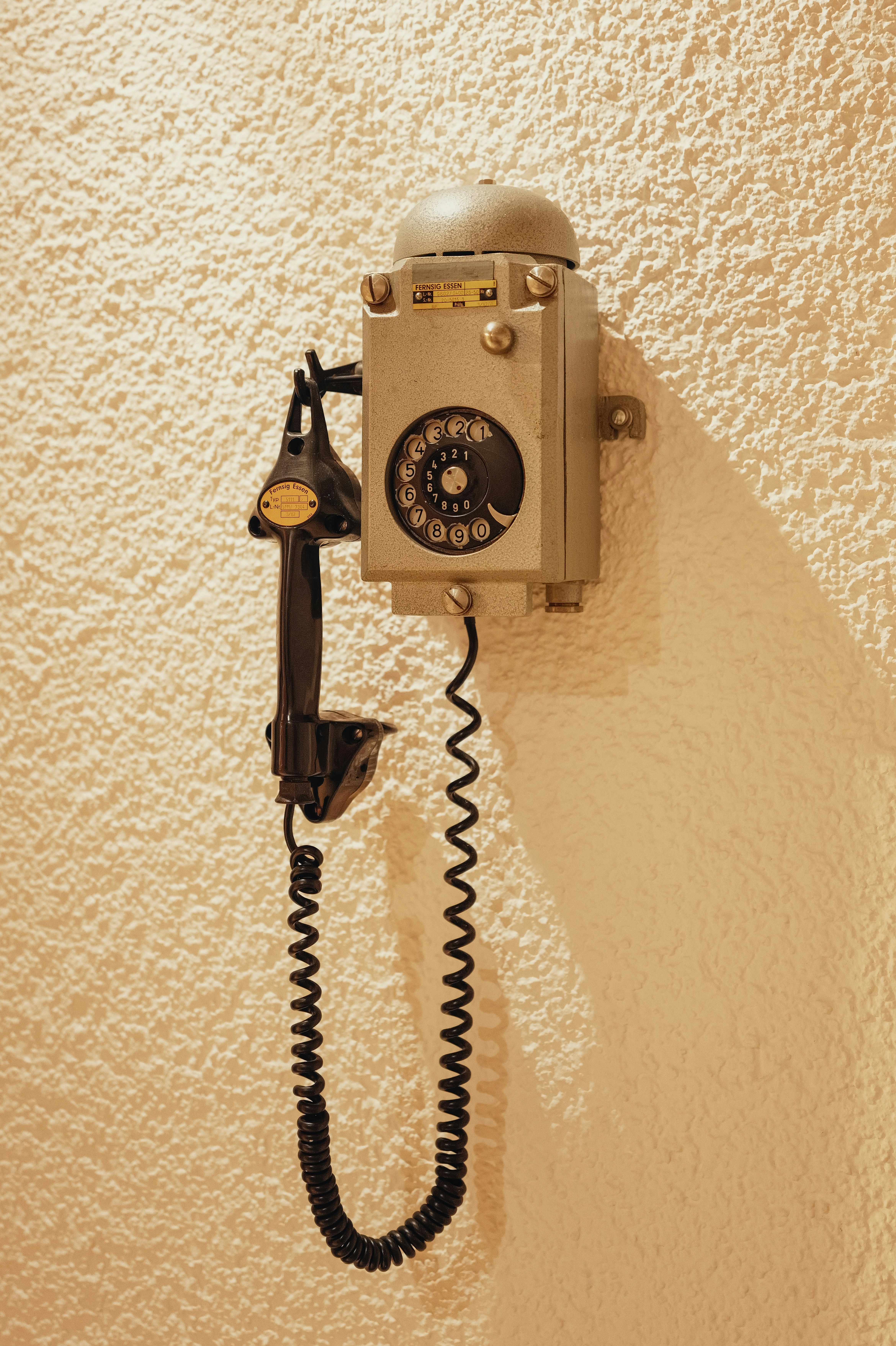 Vintage wall-mounted telephone with coiled cord and handset against a textured plaster wall, rendered in warm sepia tones.
