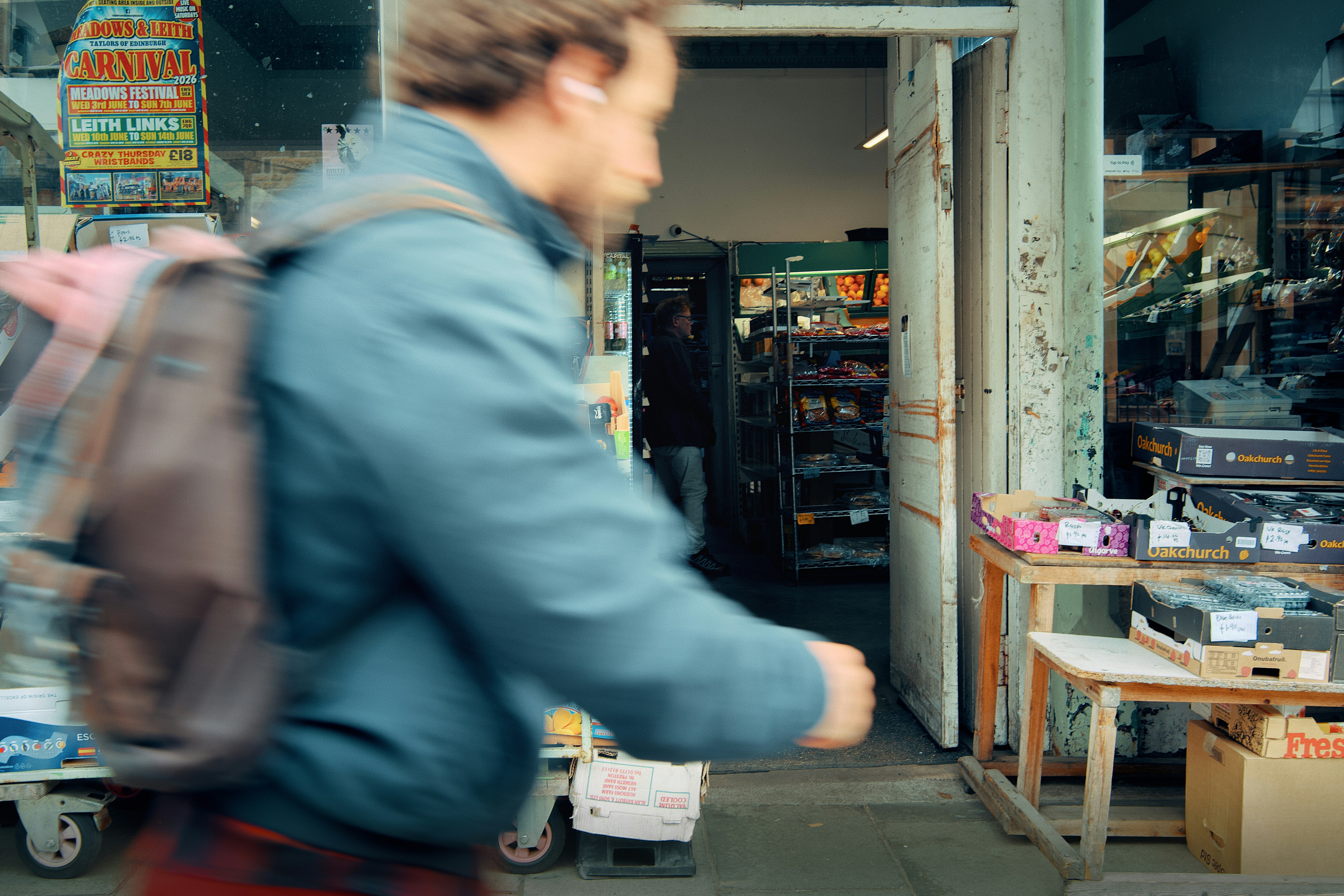 Blurred commuter entering a cluttered storefront on a busy street