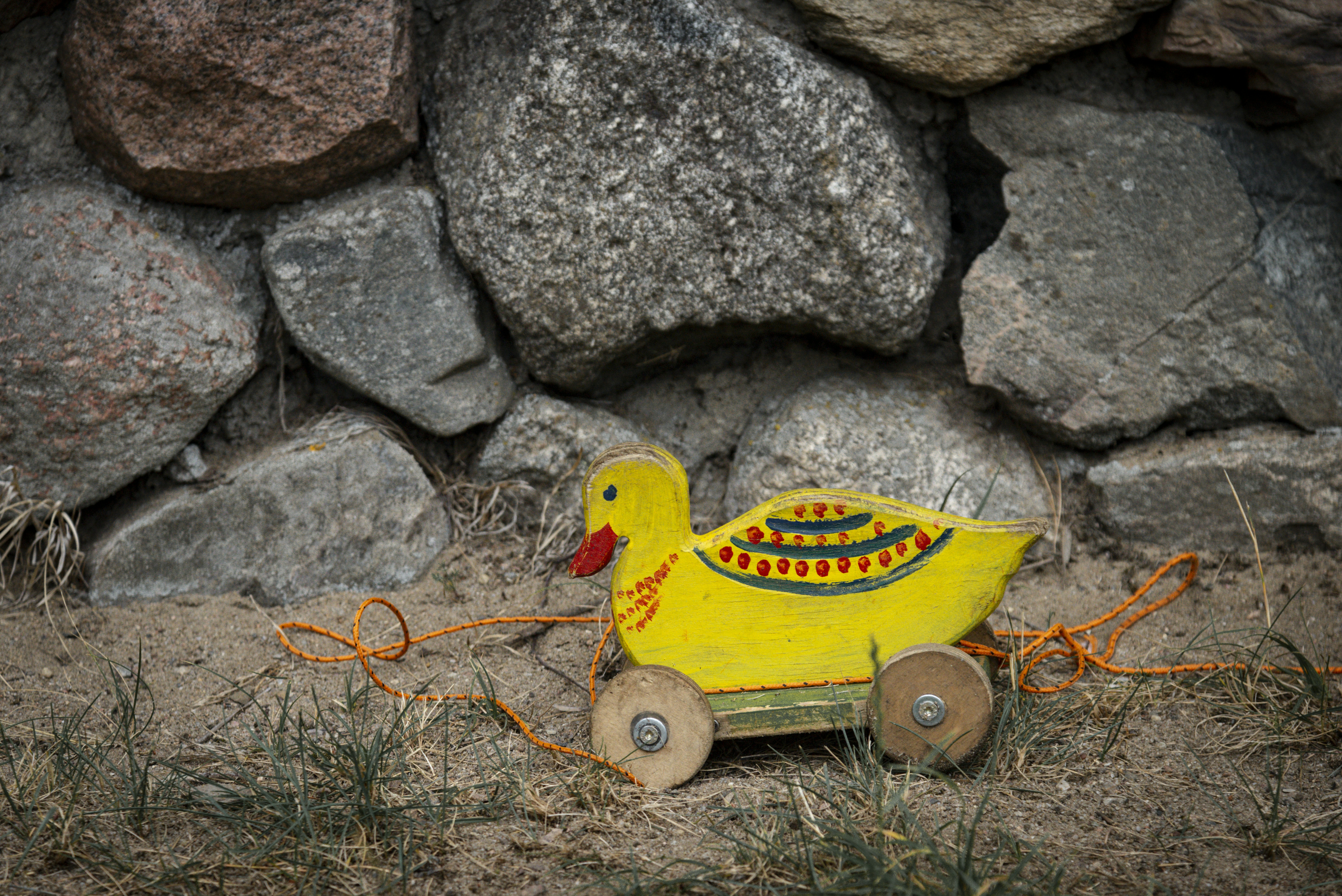 Yellow toy duck on wheels nudged by orange string against stacked stones