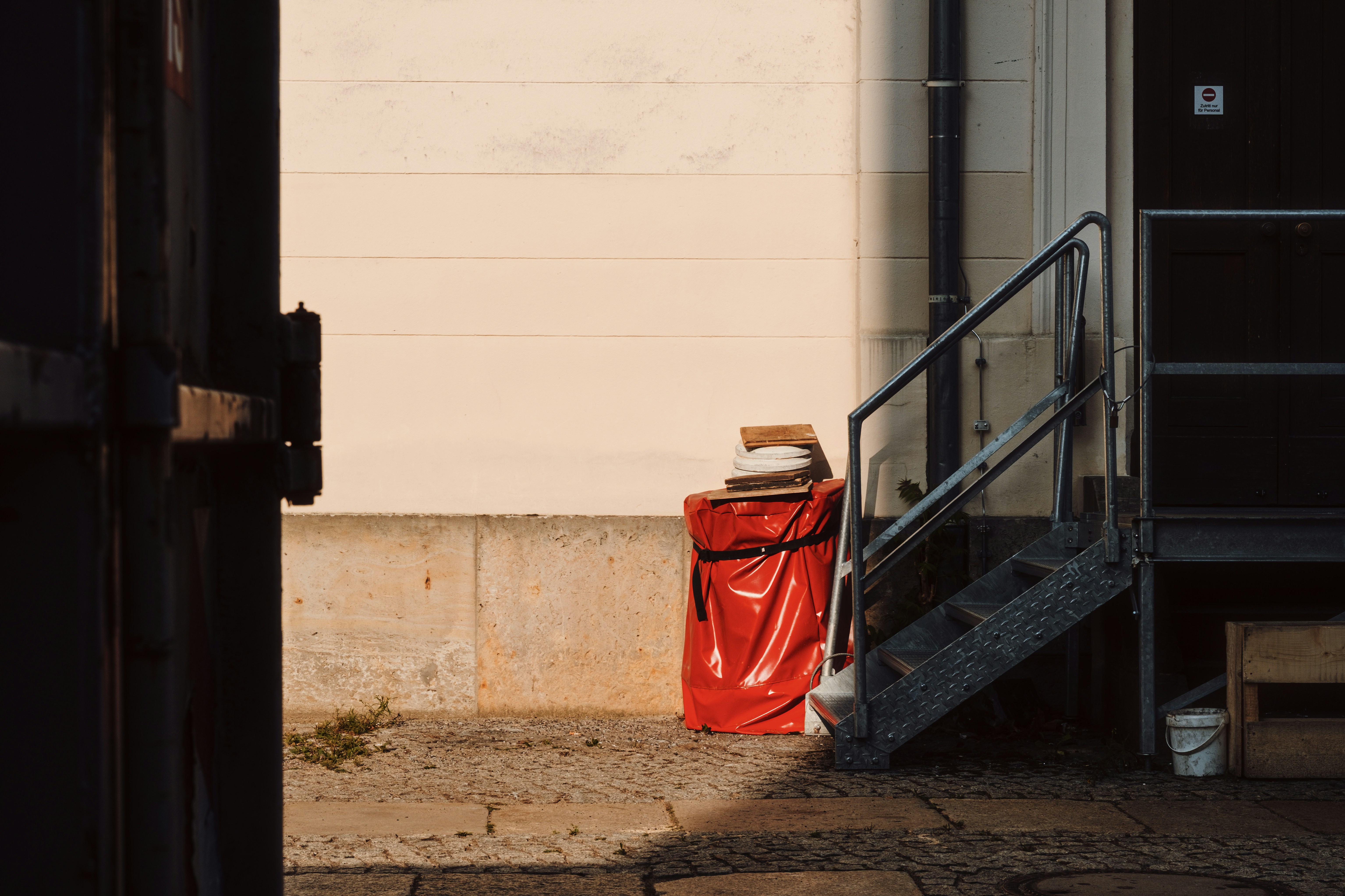 Red Trash Can by a Stairway in Dim Courtyard