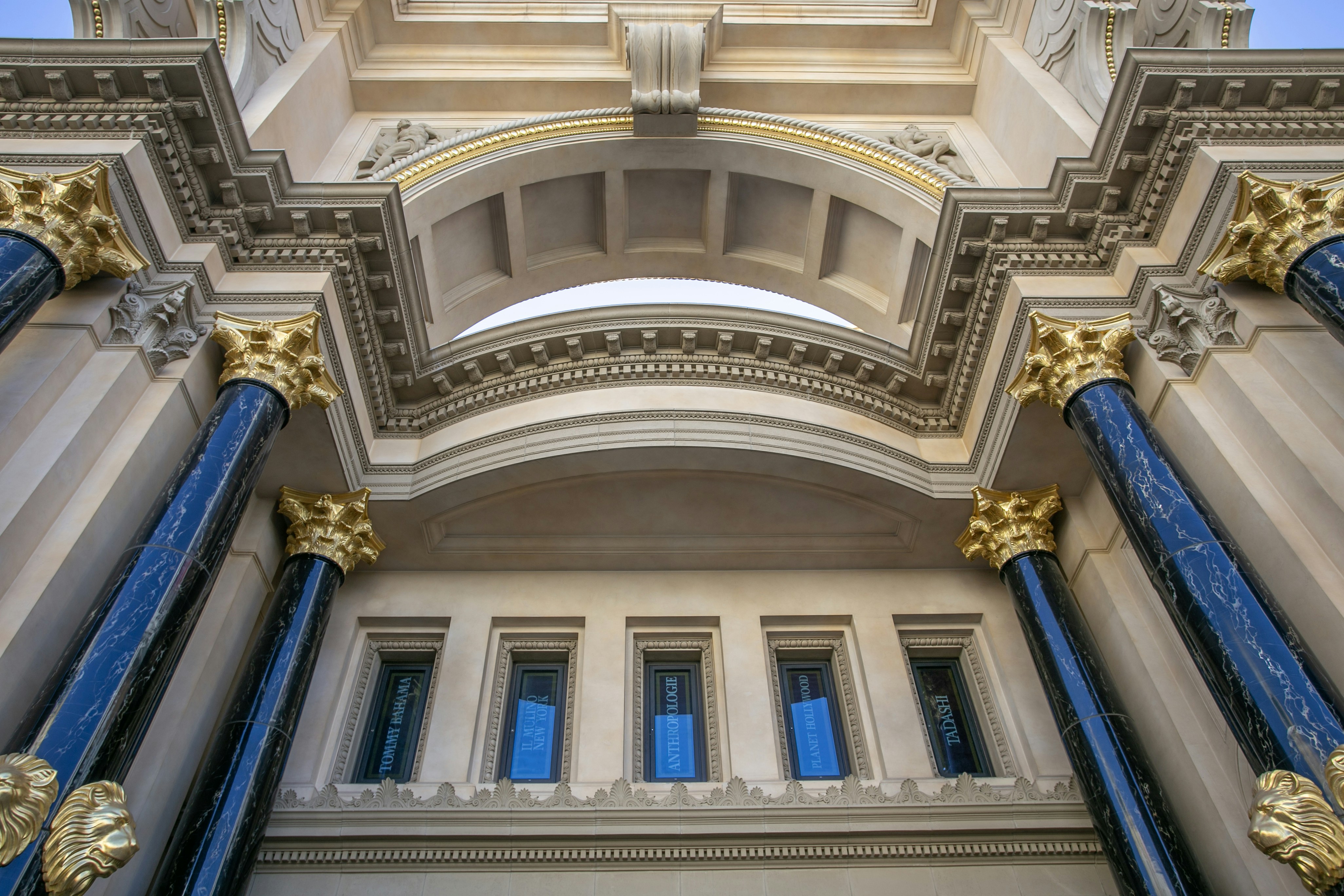 Imposing neoclassical facade with deep arches and dark blue columns topped by gold capitals, framing a row of narrow windows beneath an ornate entablature.