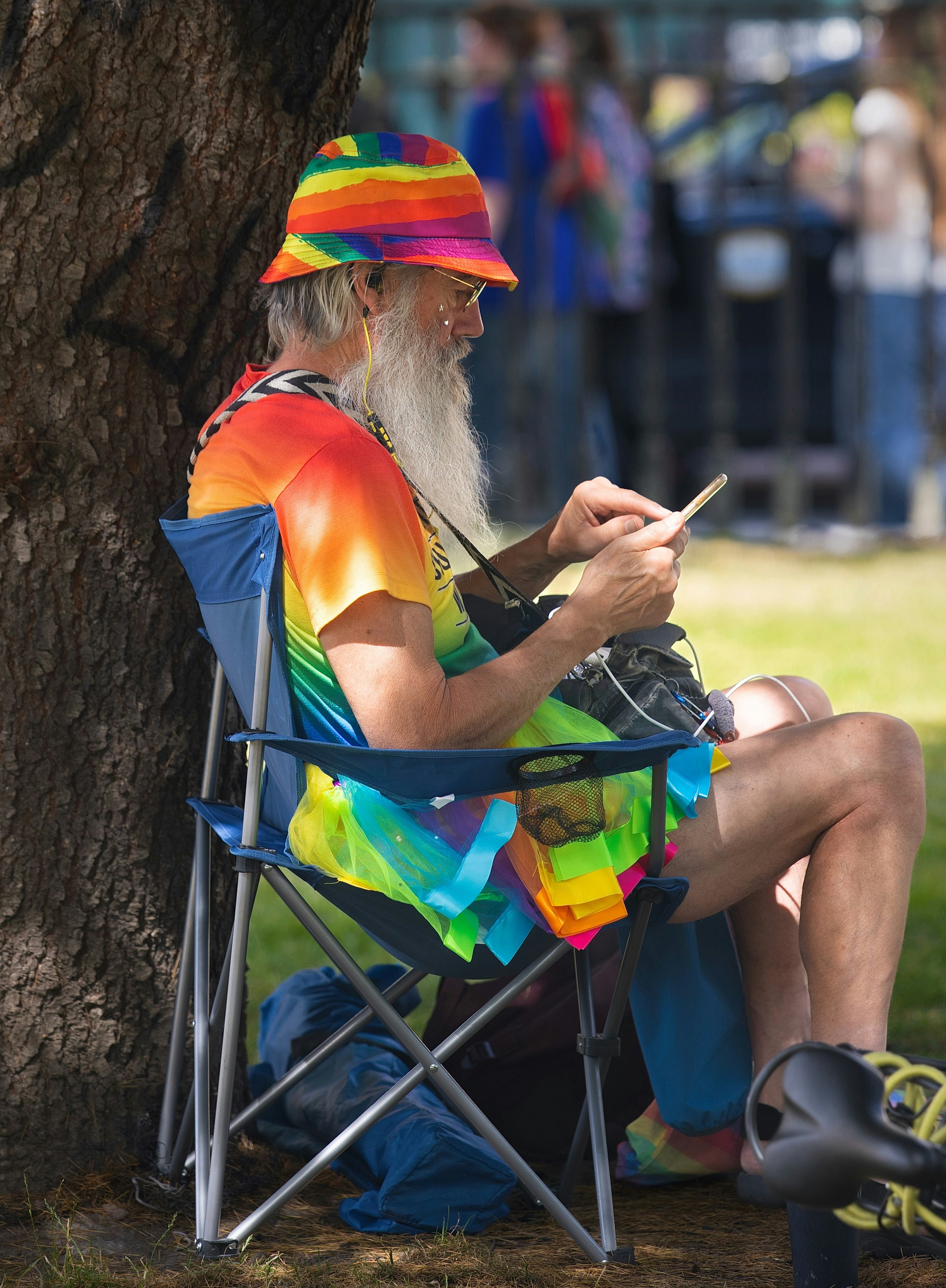 Rainbow hat, rainbow life: a man in a festival chair scrolling the world