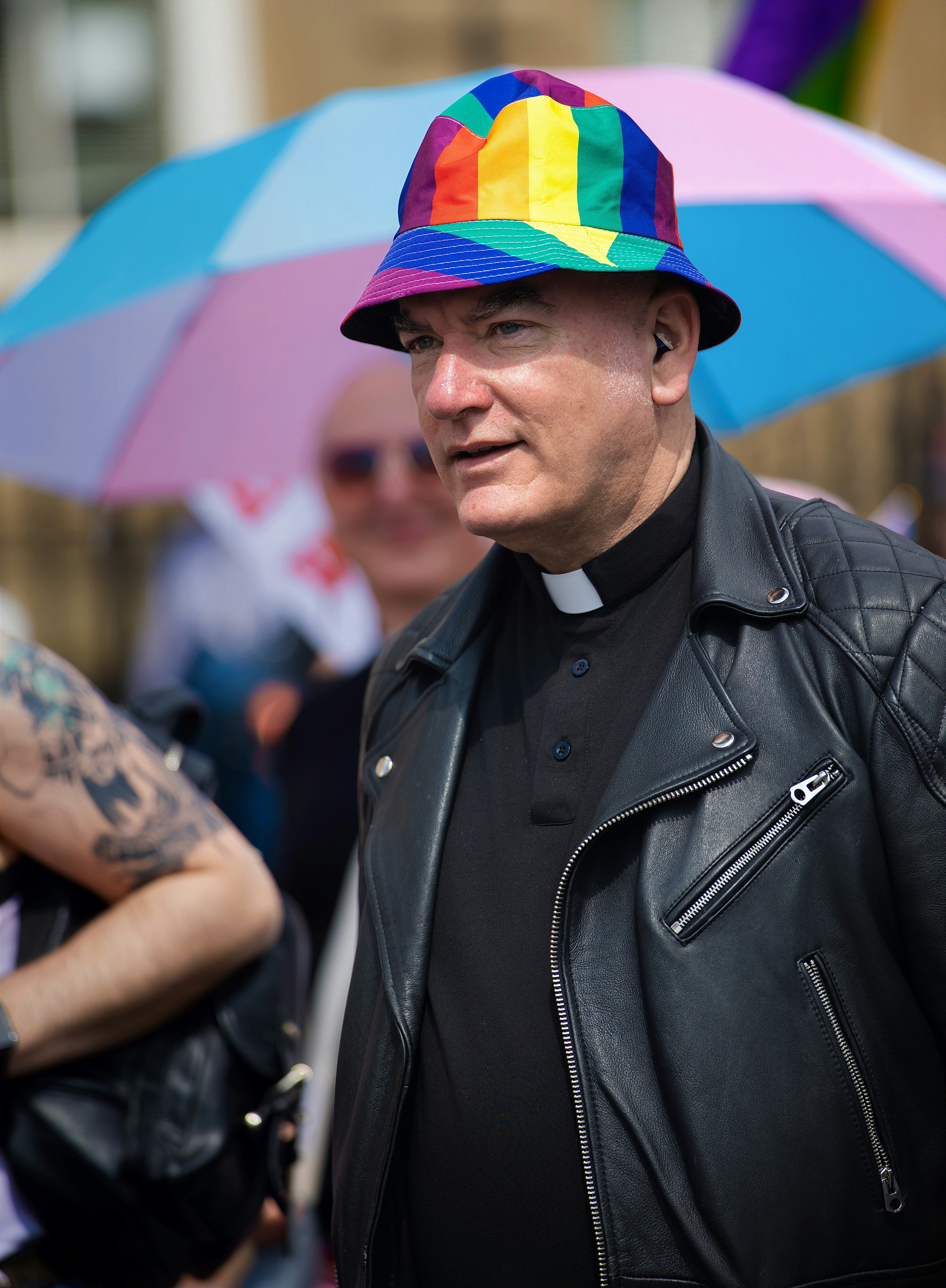 Rainbow Fedora in Focus: A Clerical Presence Under Colorful Umbrellas