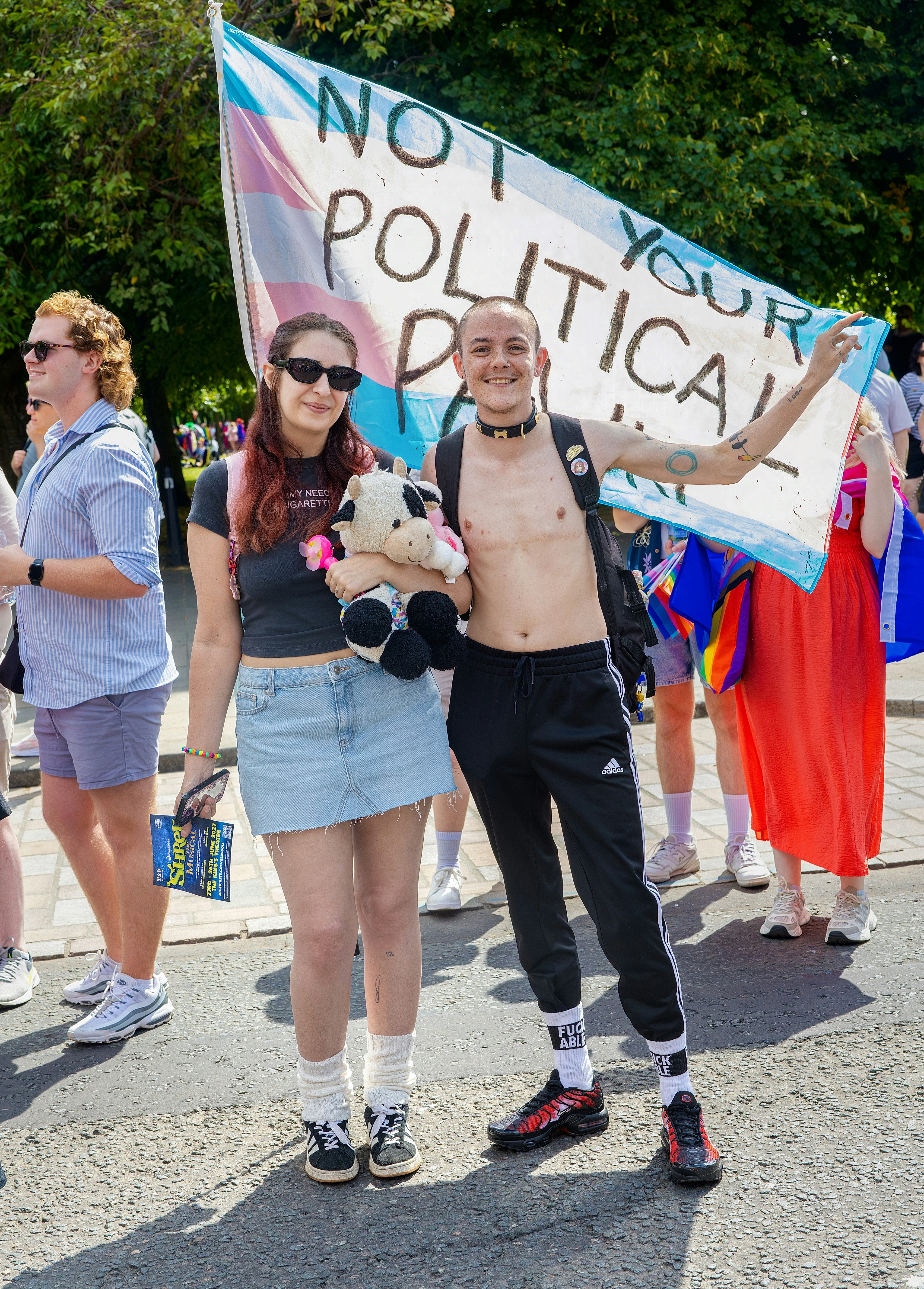 Protesters at Pride Parade Hold Banner and Hug with Plush Bear