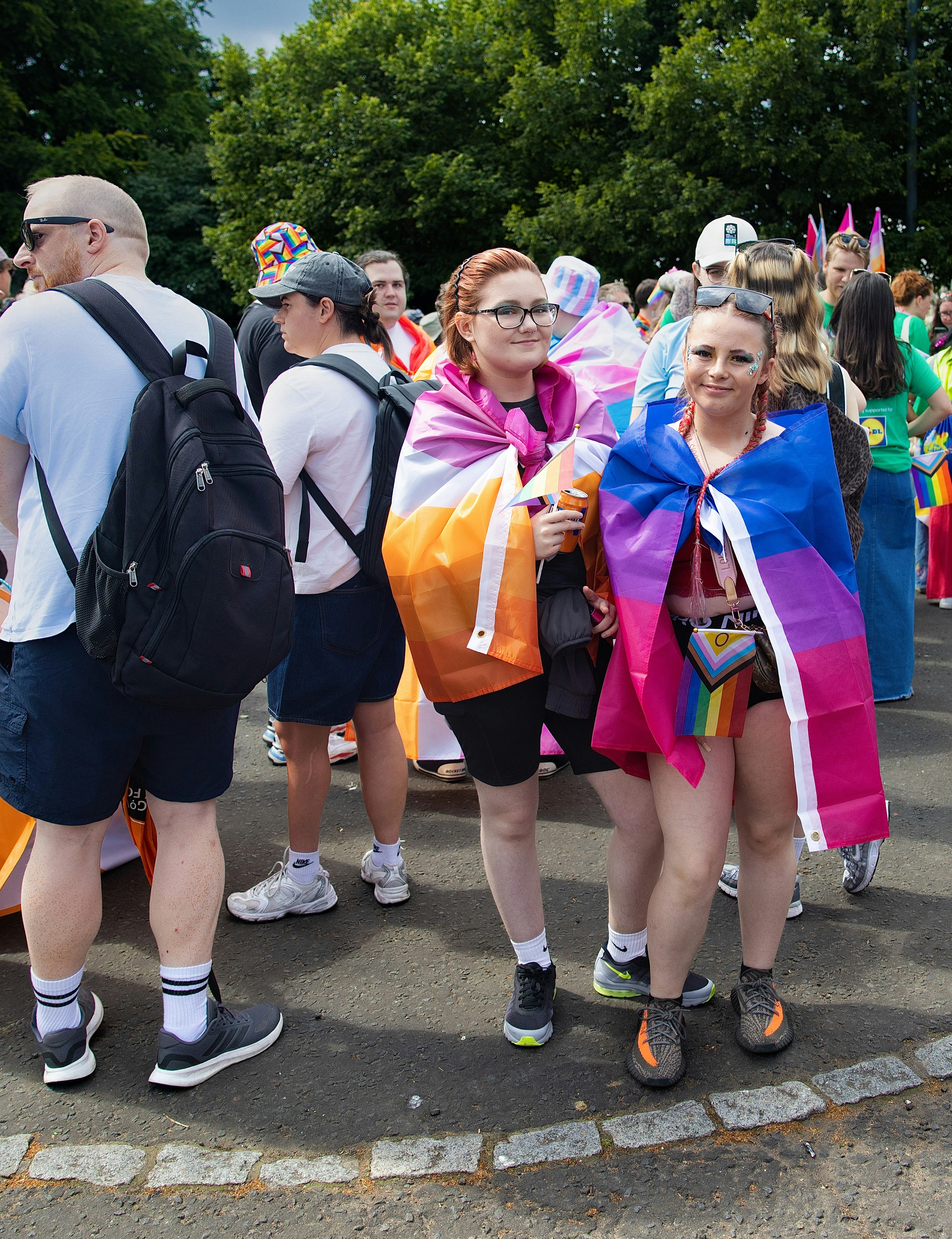 Rainbow Pride at the Parade: Two friends wrapped in colorful flags stand among the crowd