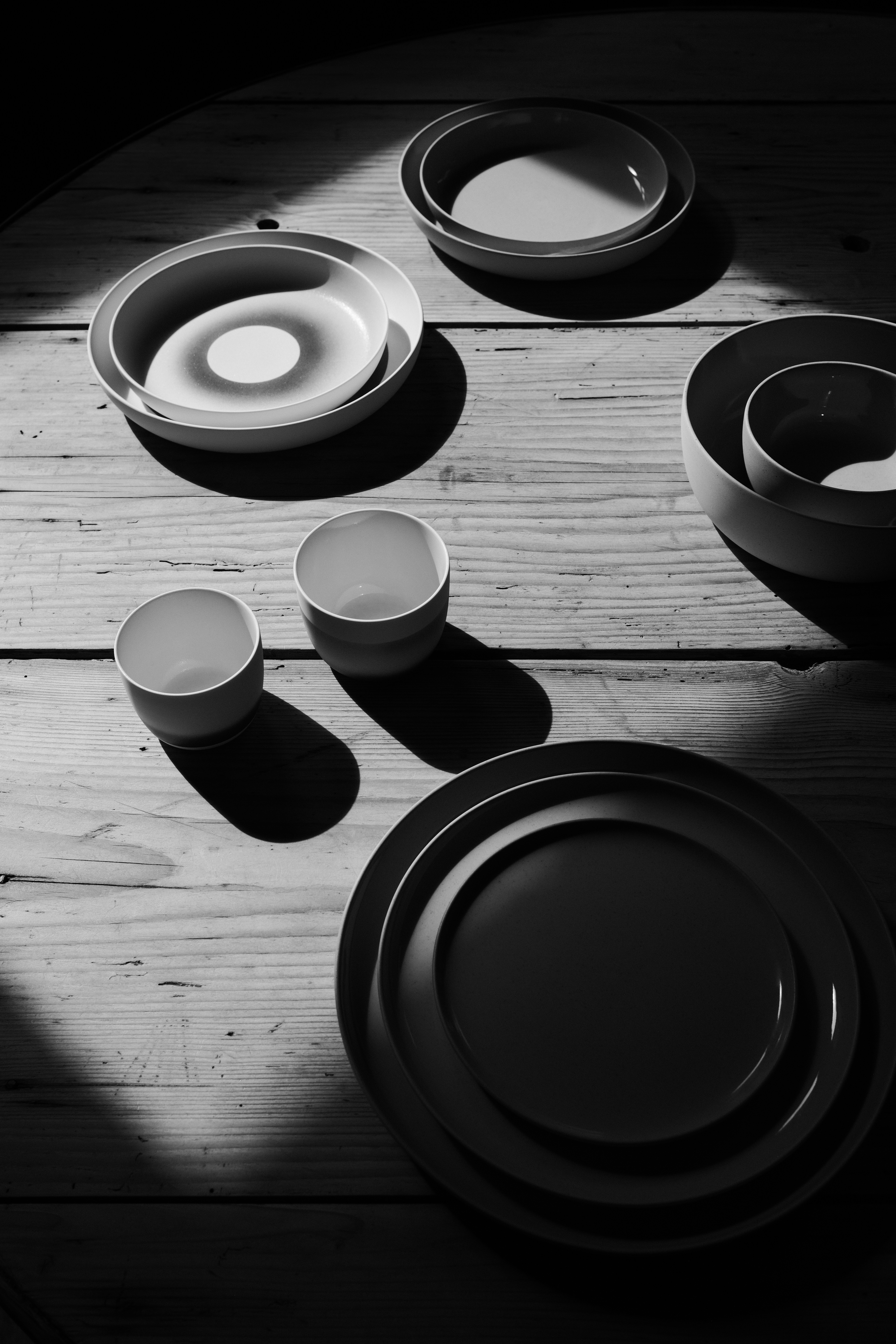 Shadowed Still Life: Ceramic Discs and Cups on Weathered Wood