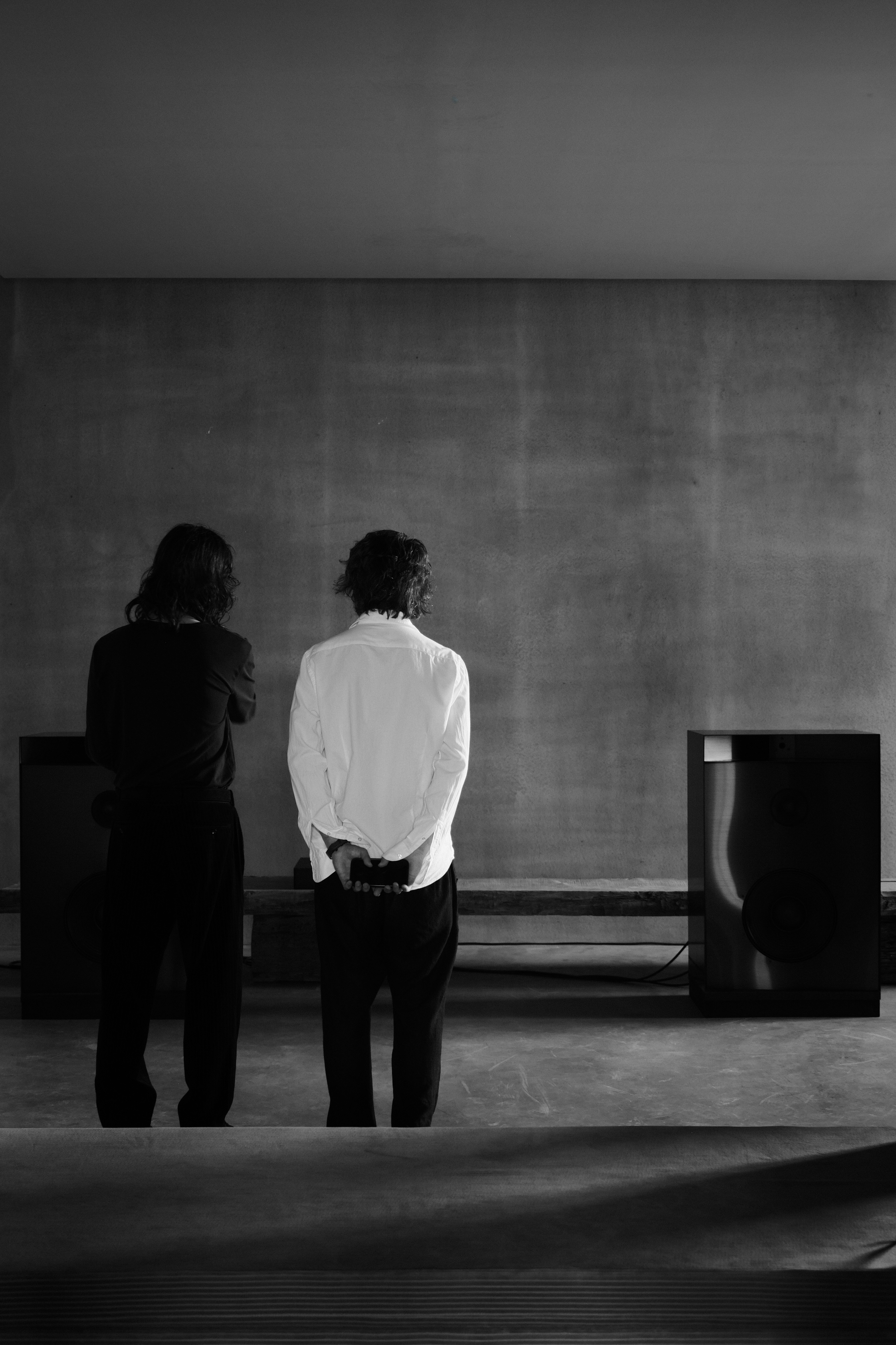Two Figures in Shadowed Gallery: Silent Conversation Beneath Concrete Light