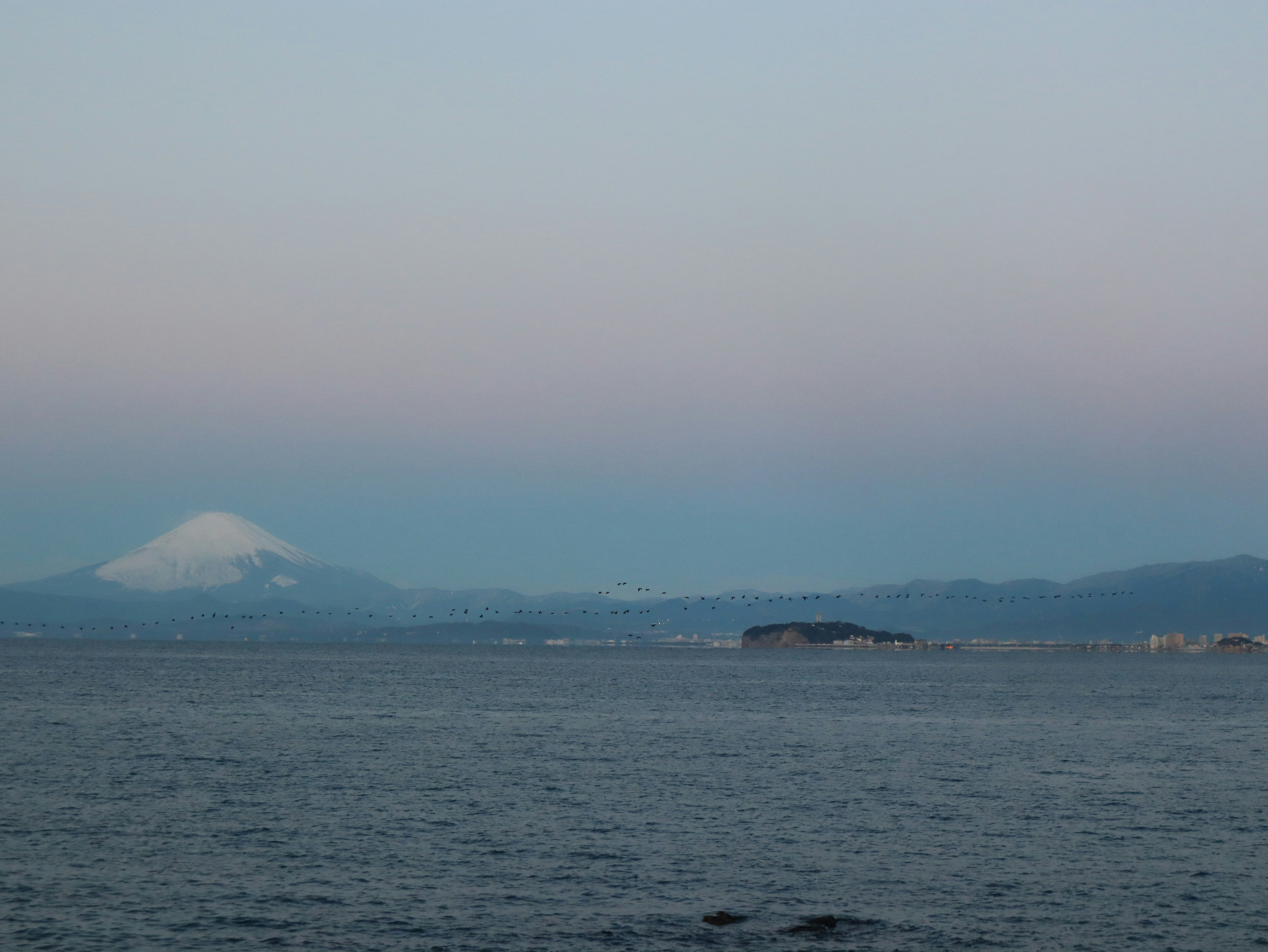 Silent Horizon: Snow-Capped Peak Behind a Calm Sea