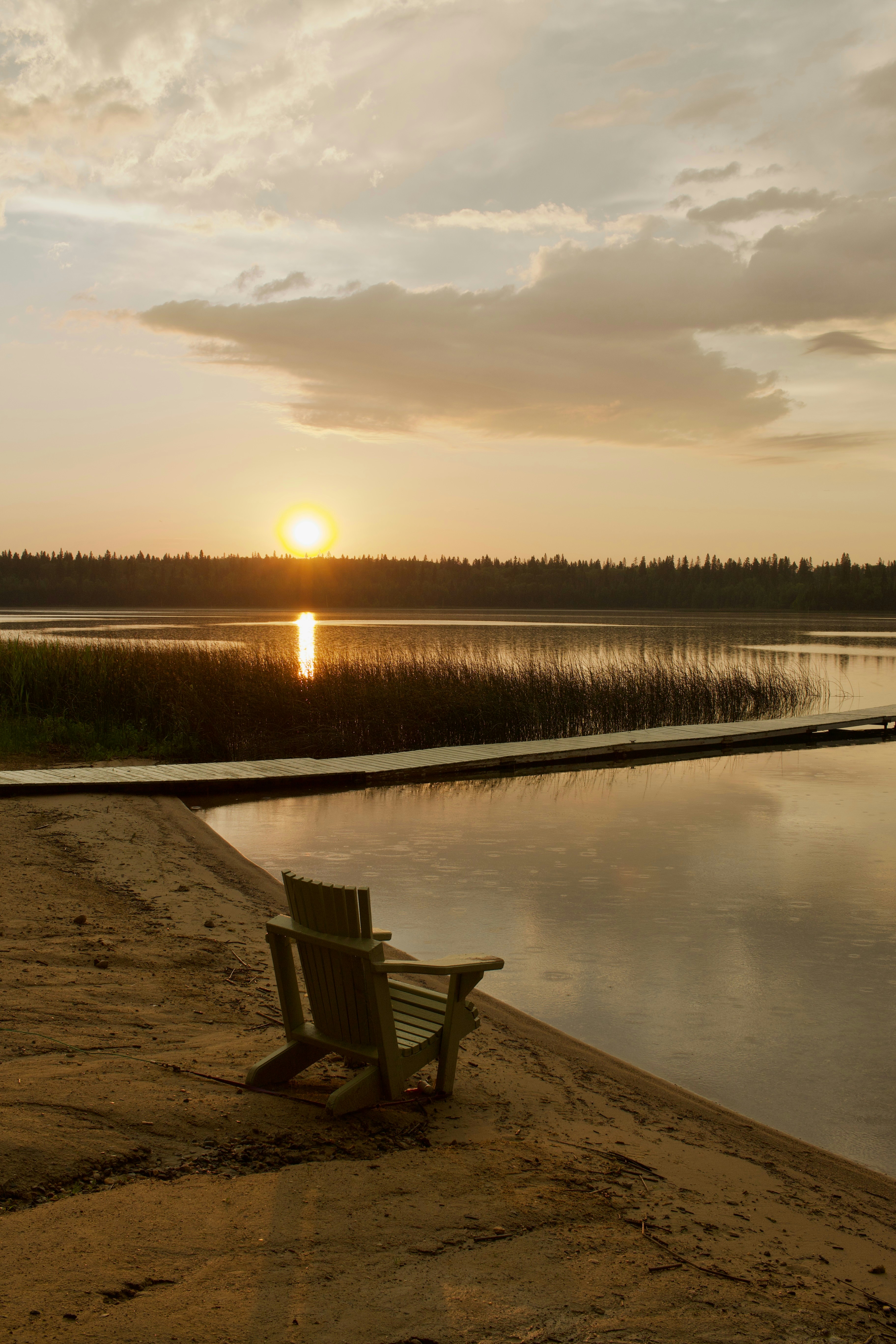 Sunlit Quiet: A Wooden Chair by a Serene Lake at Dusk
