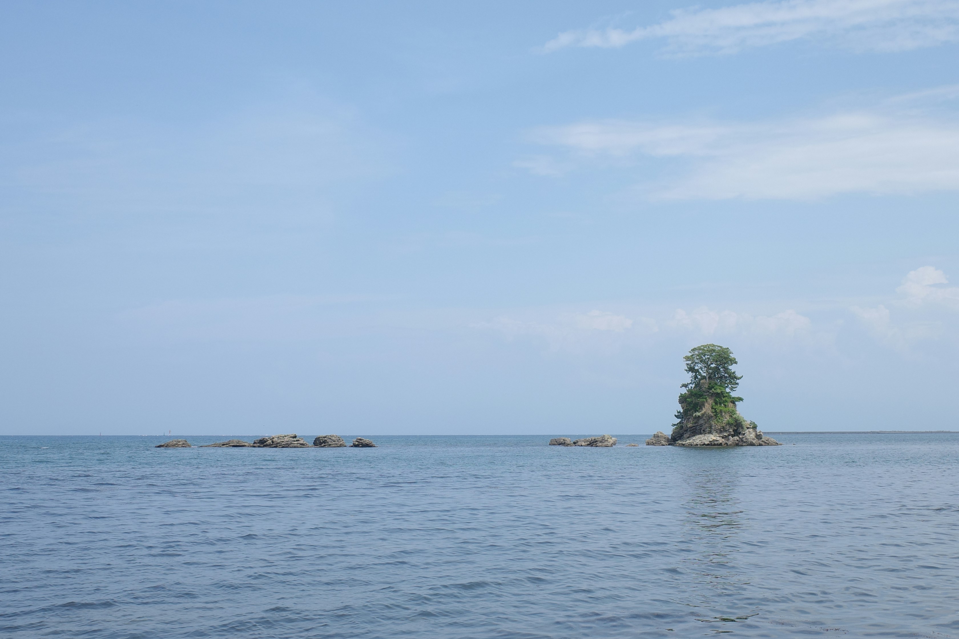 A lone pine on a distant islet amid calm sea