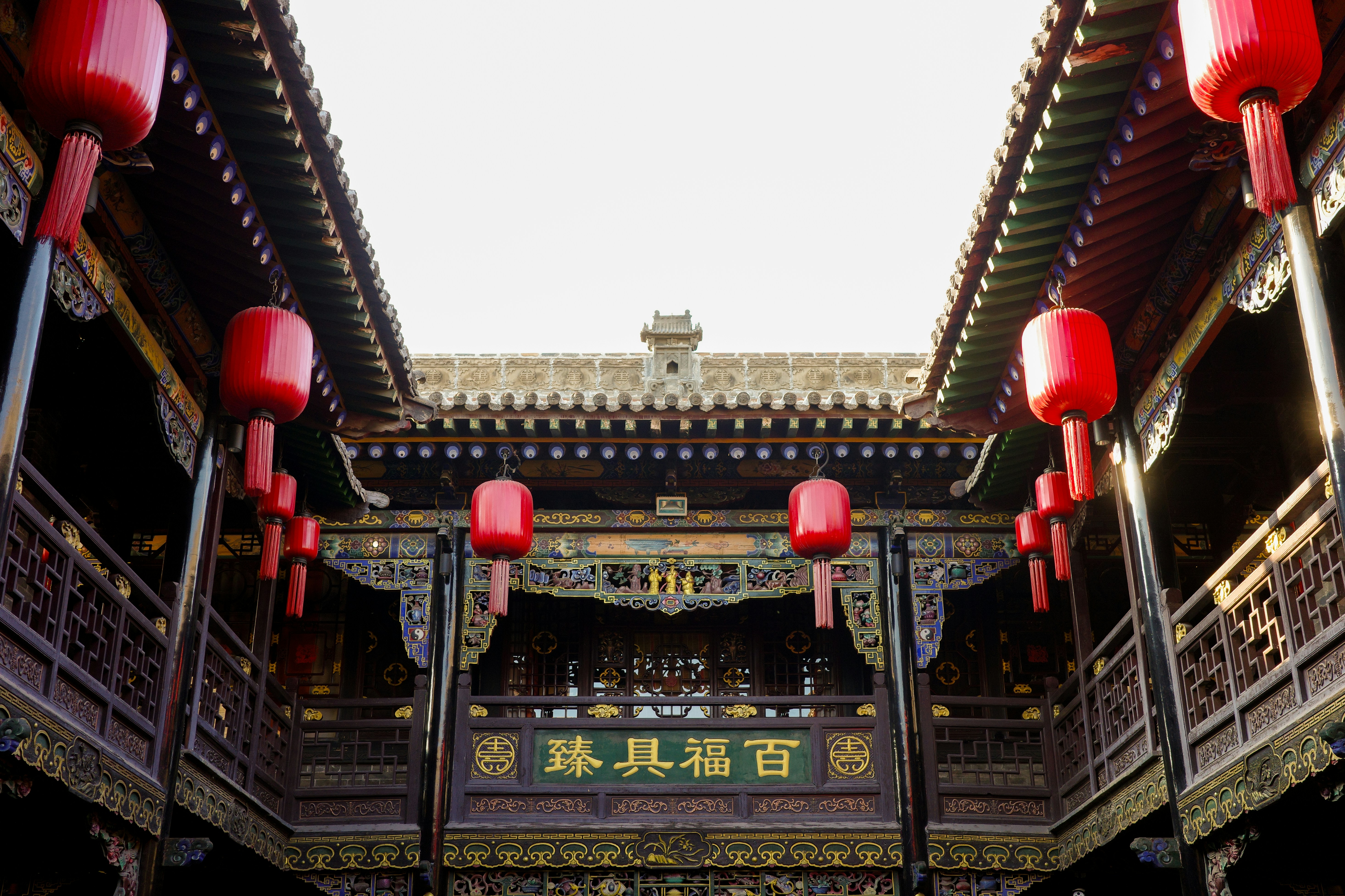 Red Lanterns Above an Intricately Carved Courtyard Gate