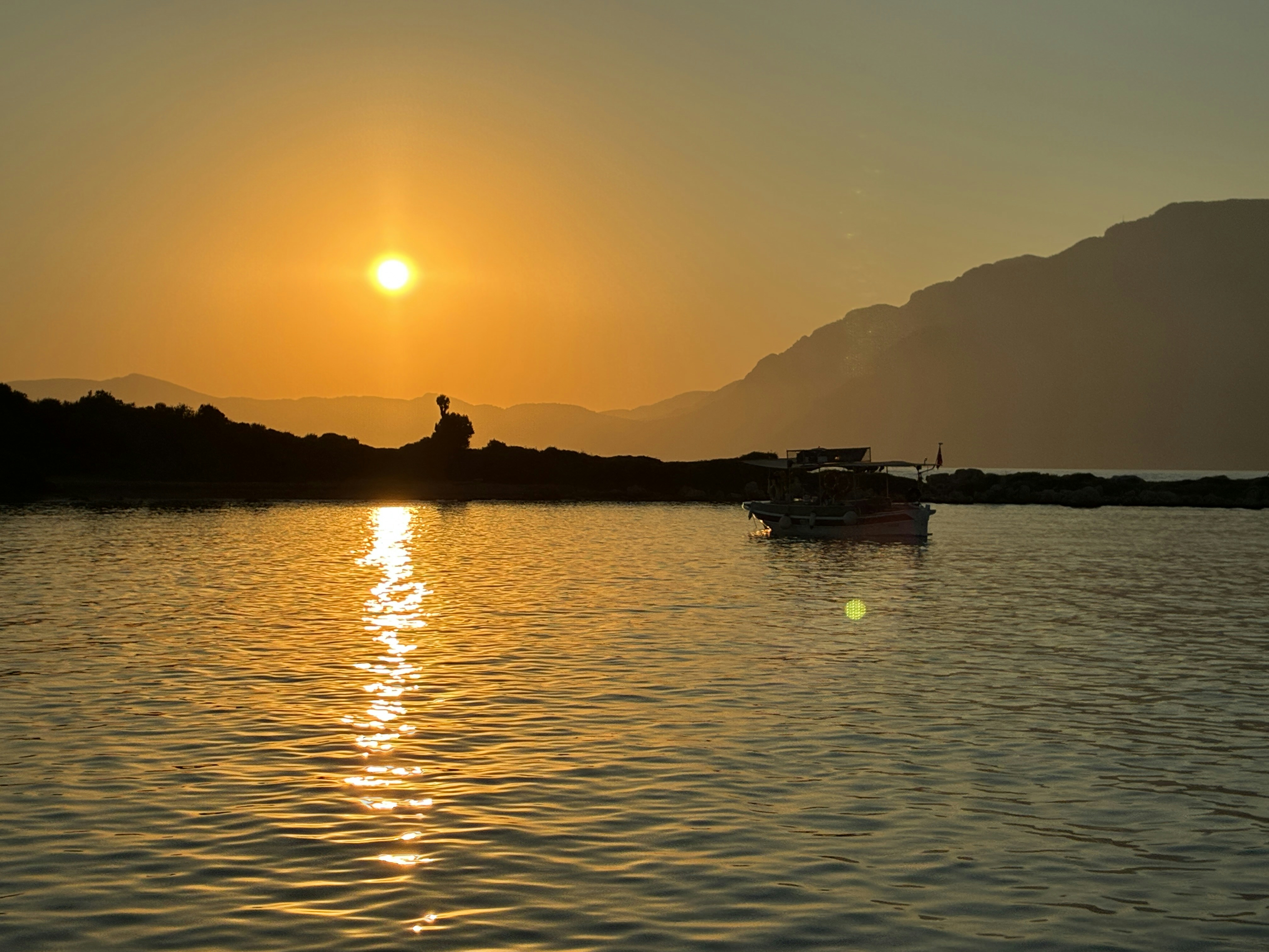 Sunlit Horizon: Boat at Dusk Beneath Golden Peaks