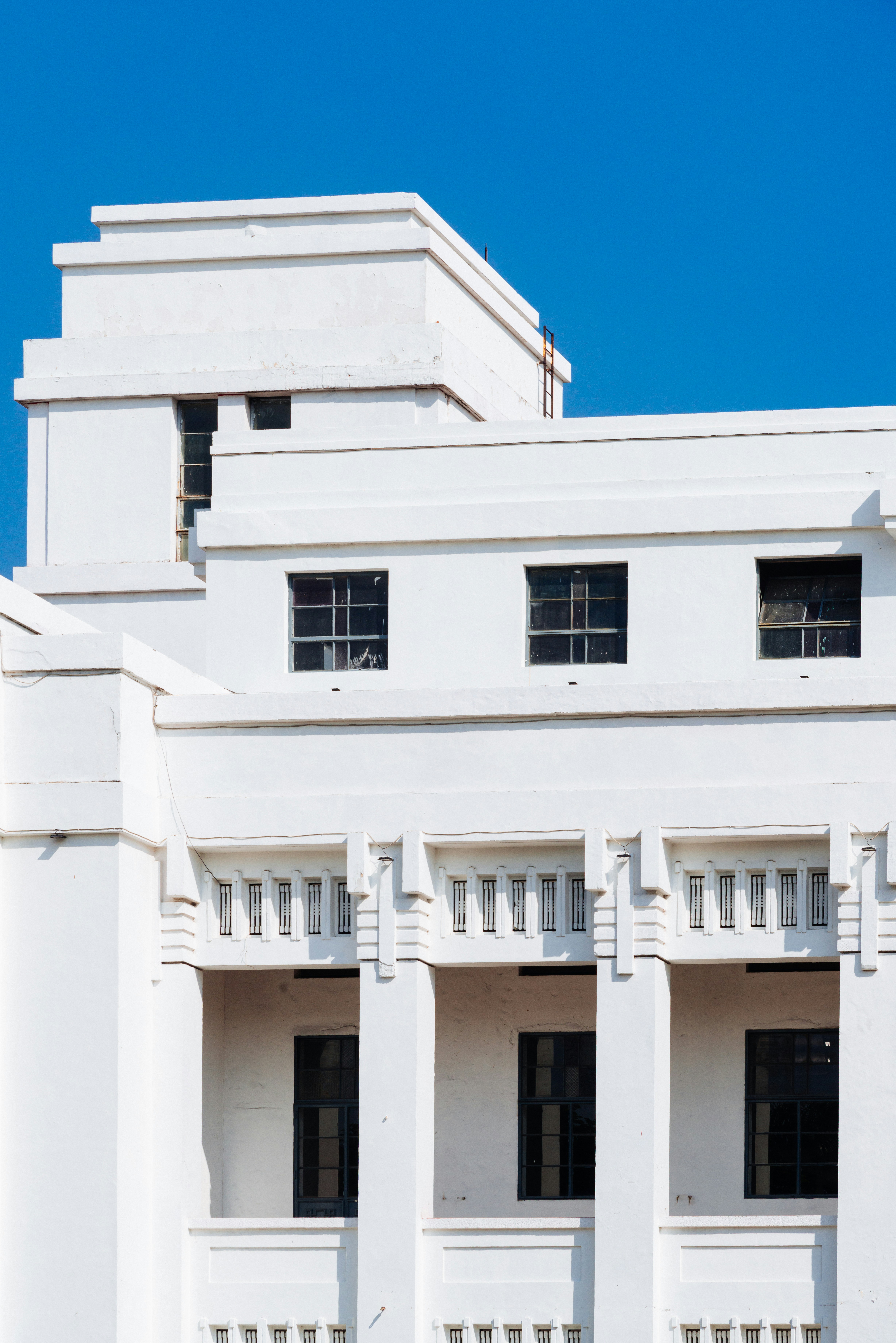 Angular white concrete blocks rise against a vivid blue sky, revealing a modernist facade with rectangular windows and decorative balustrades.