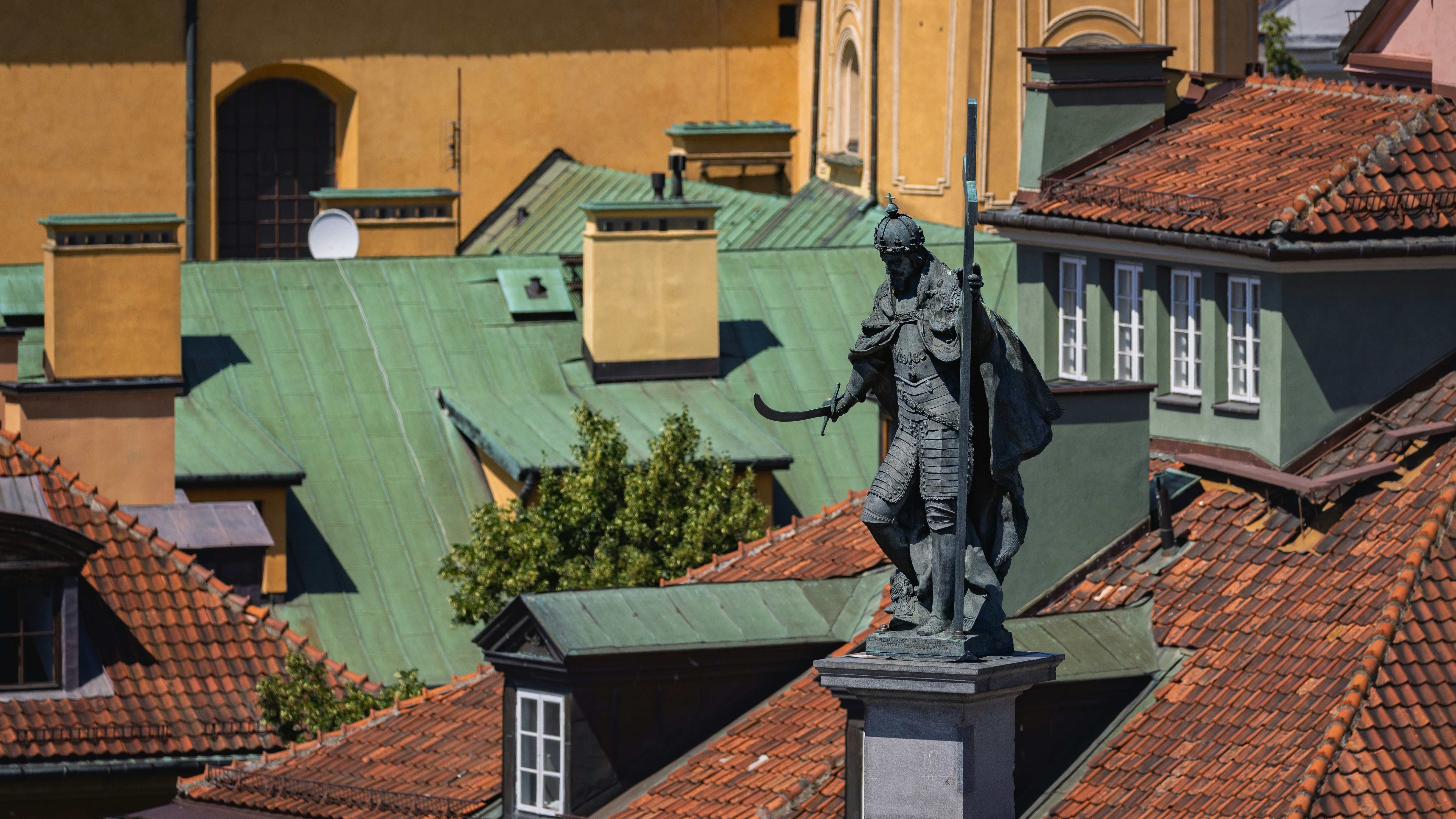 Historical statue stands above colorful european city rooftops.