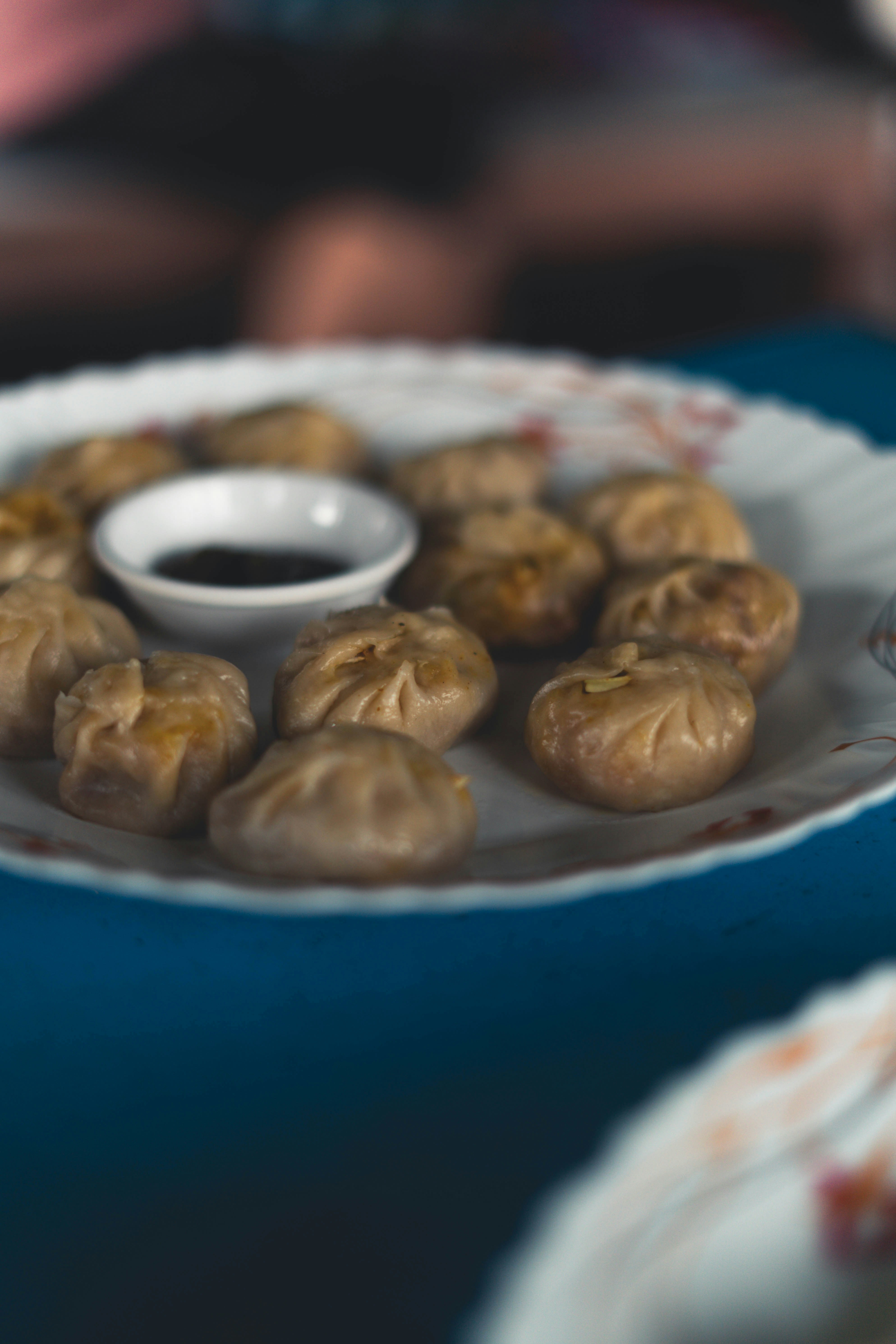 Plate of steamed dumplings with a dipping sauce on a teal table