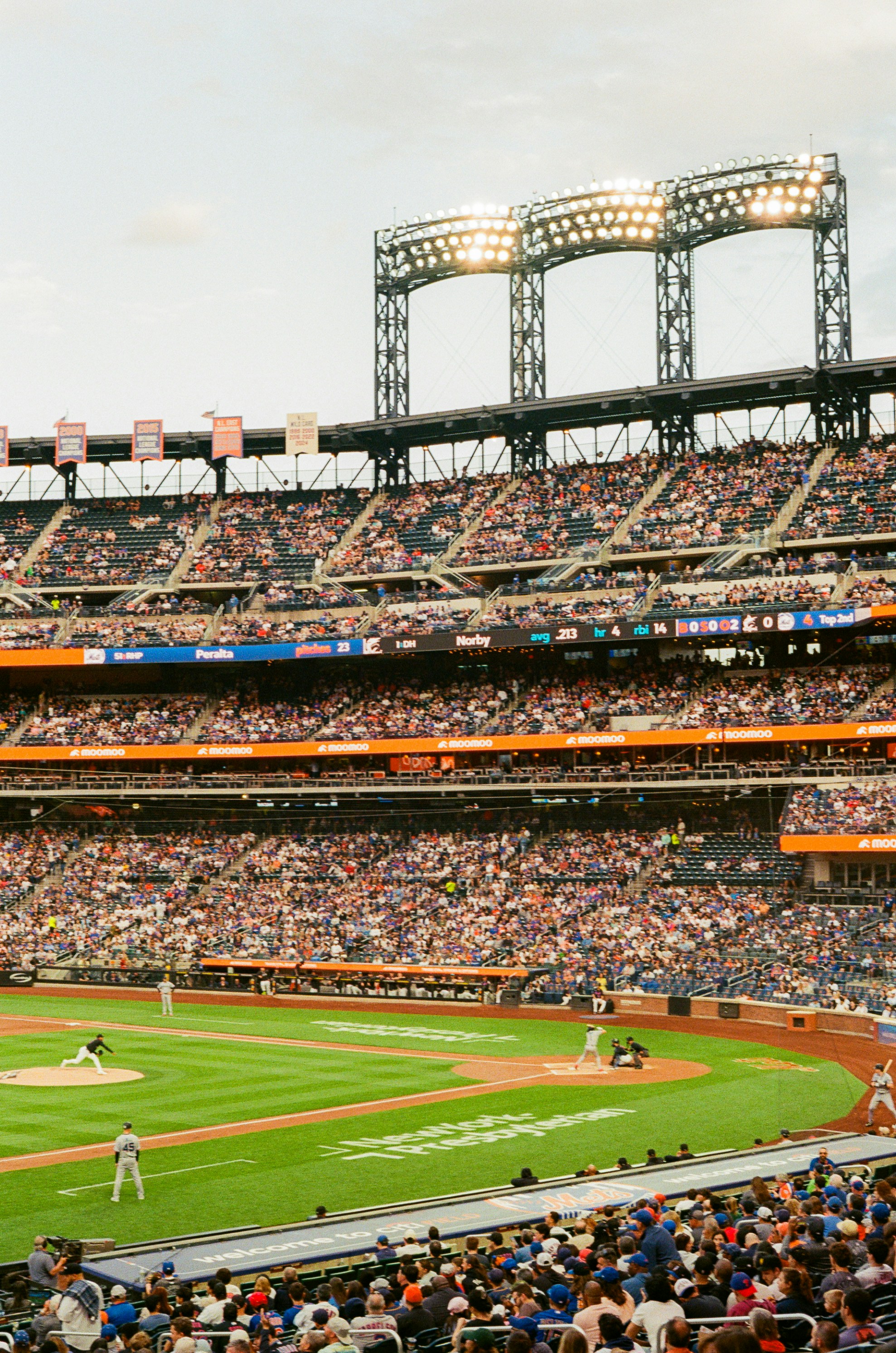 A crowded baseball stadium captured on film during a game, with bright field lights, packed stands, and a timeless American summer atmosphere.