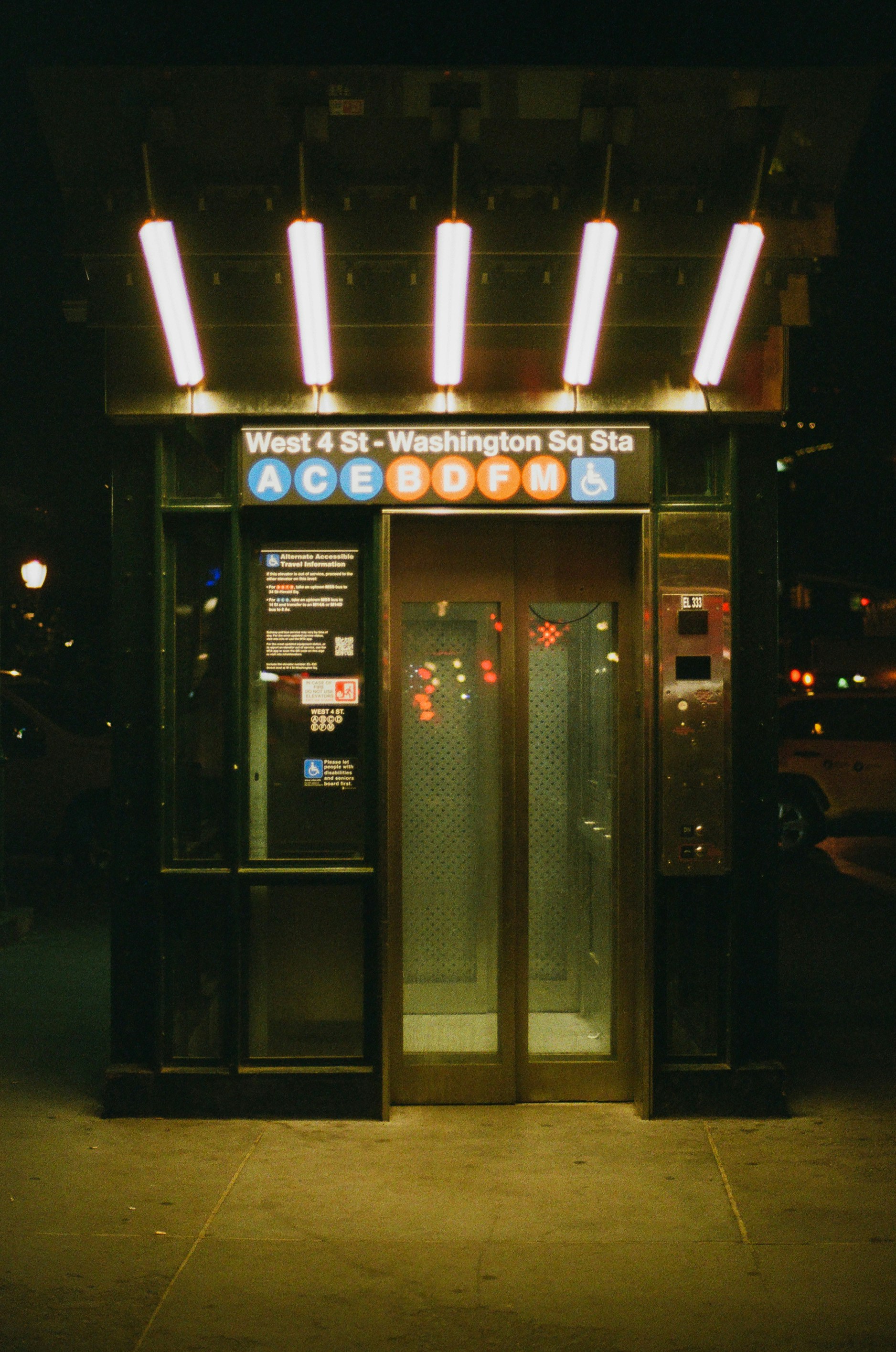 A softly lit New York City subway entrance at night, captured on film with glowing lights, deep shadows, and a quiet nostalgic atmosphere.