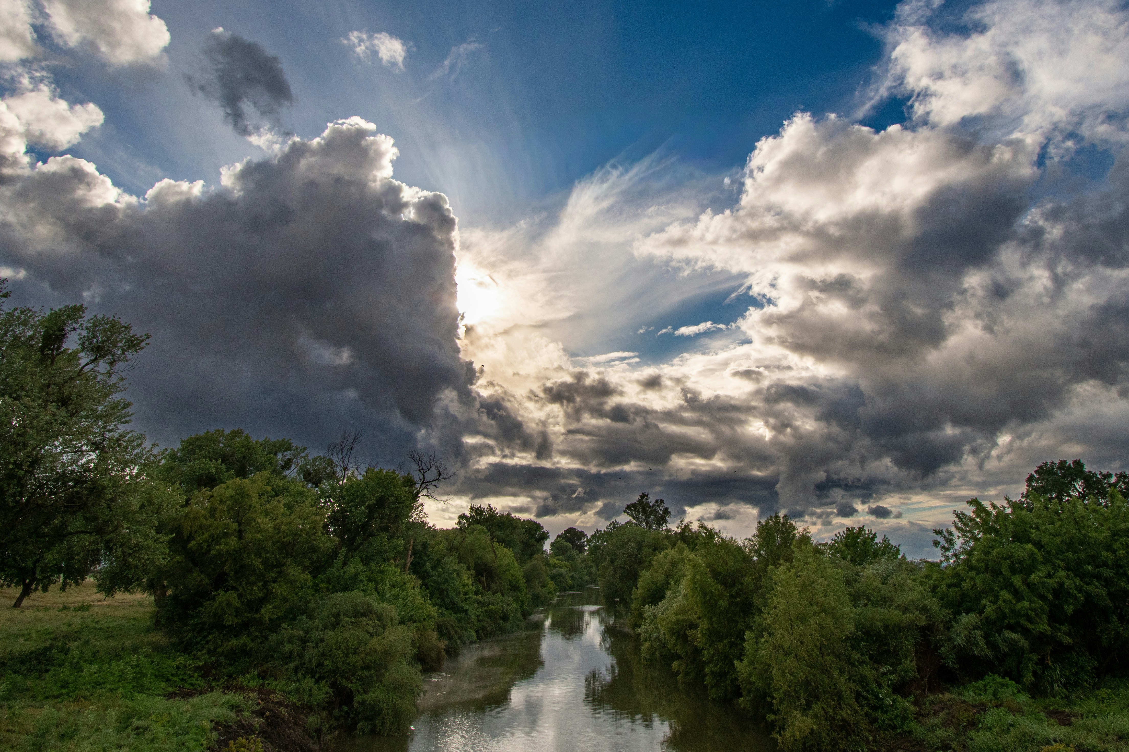 Vast river bend flanked by trees under a dramatic sky with sunlit breaks.