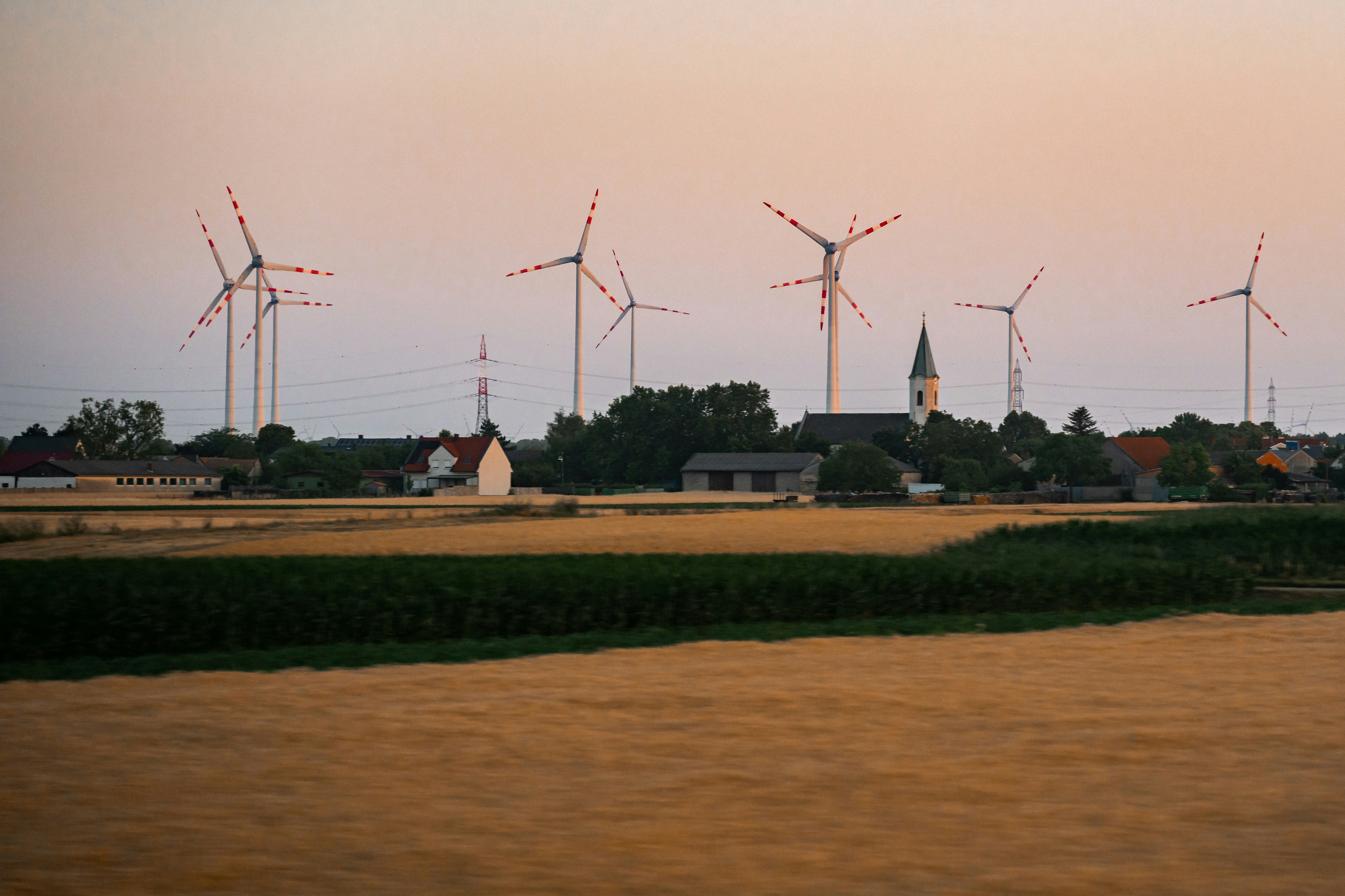 Wind turbines and a village at sunset over golden fields.