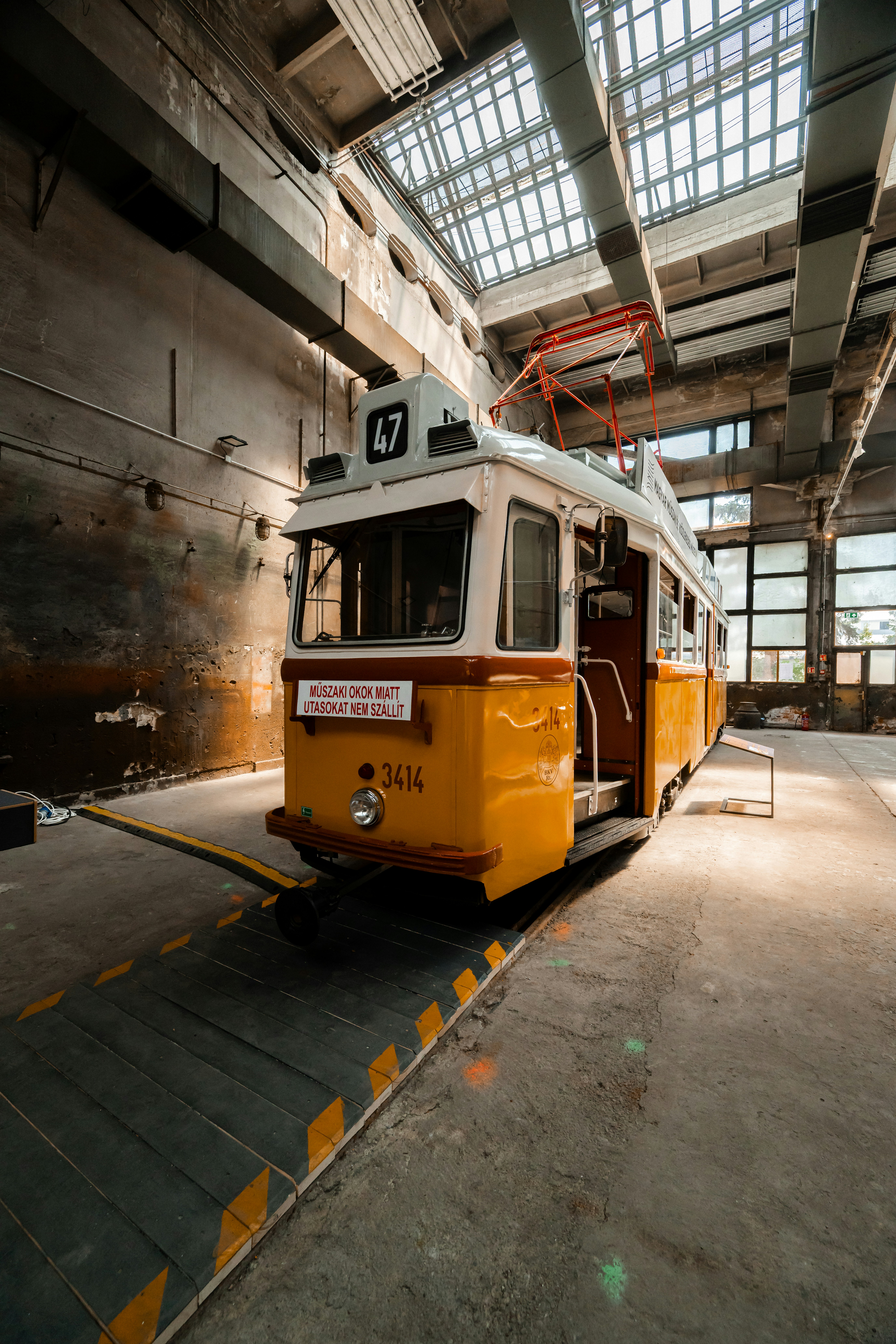 Yellow tram in a sunlit industrial depot awaiting restoration