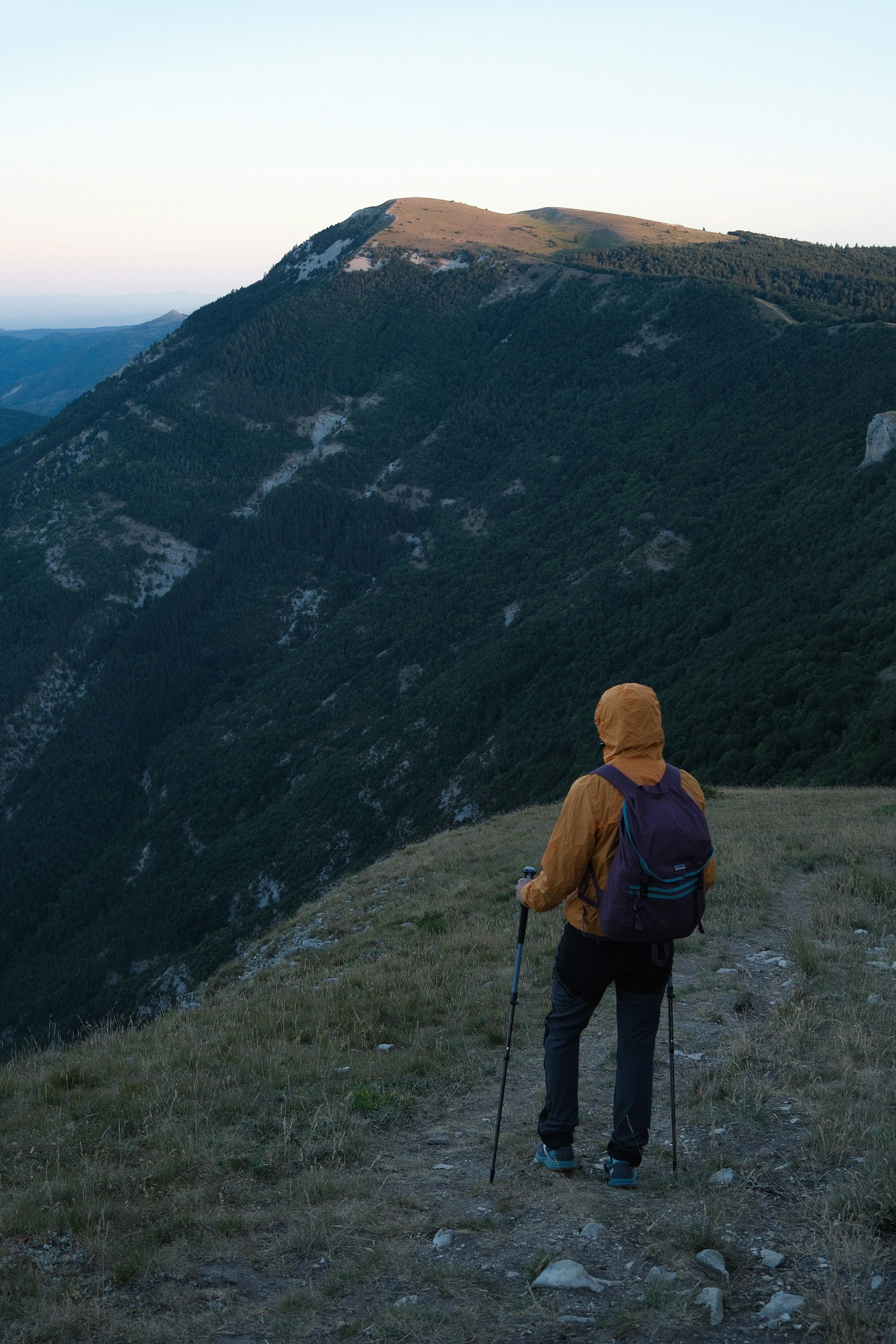 On the Edge: A Hiker Climbing Toward Distant Peak at Twilight