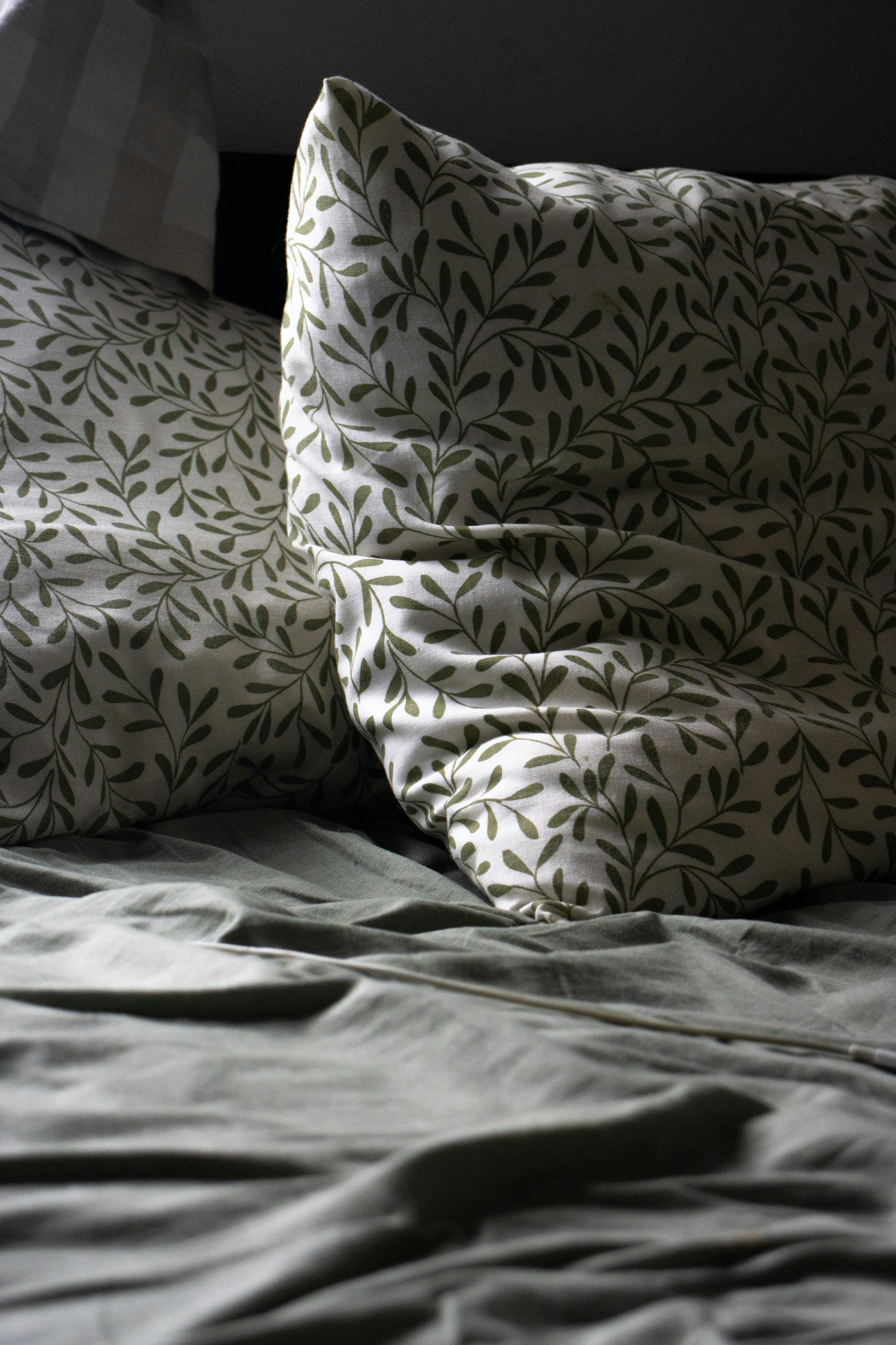 Cushioned Quiet: Leafy Patterned Pillow Nestled on Crumpled Gray Bed Linen