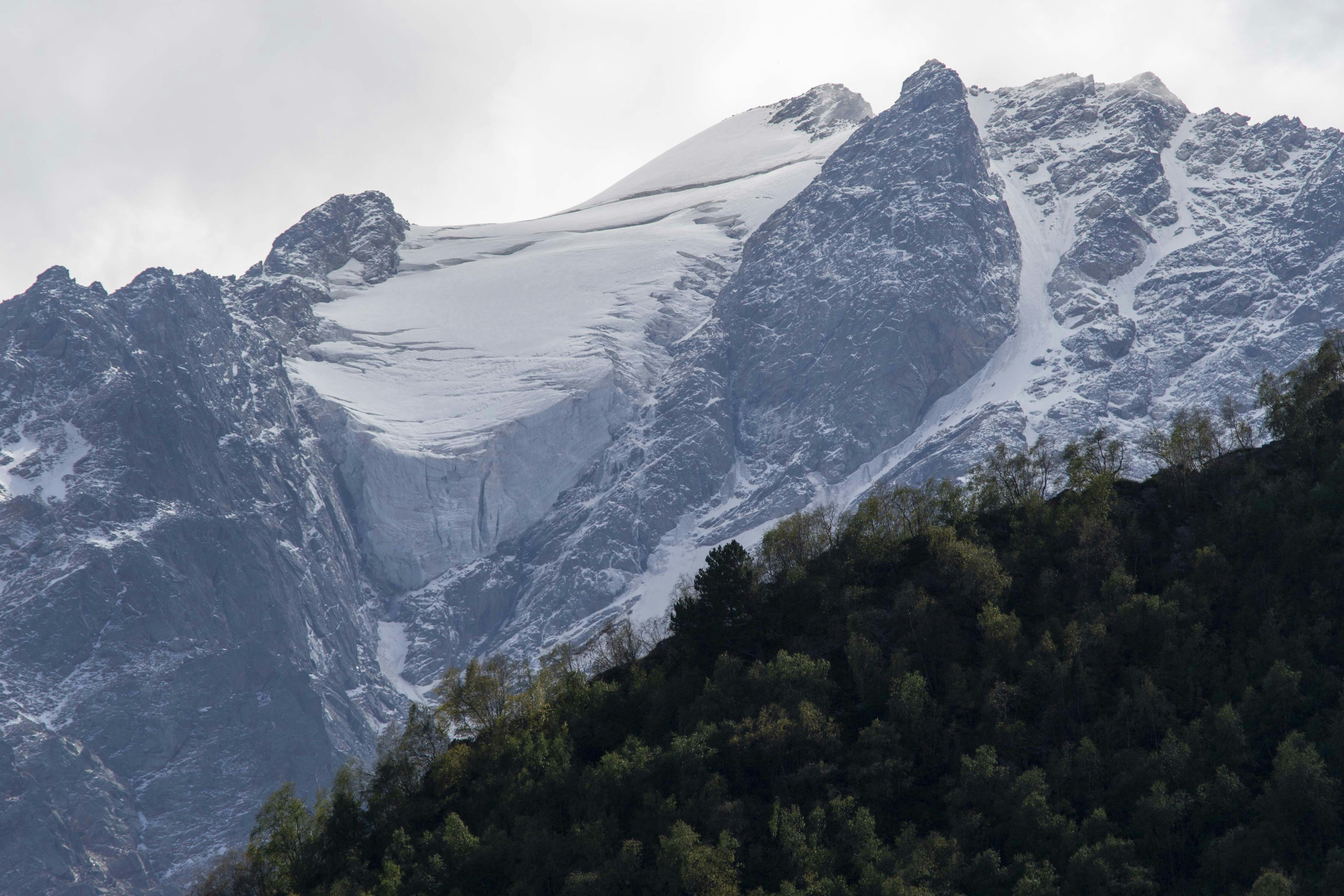 Snow-dusted alpine peak above a dark conifer forest, captured with emphasis on the rugged summit and glacial textures.