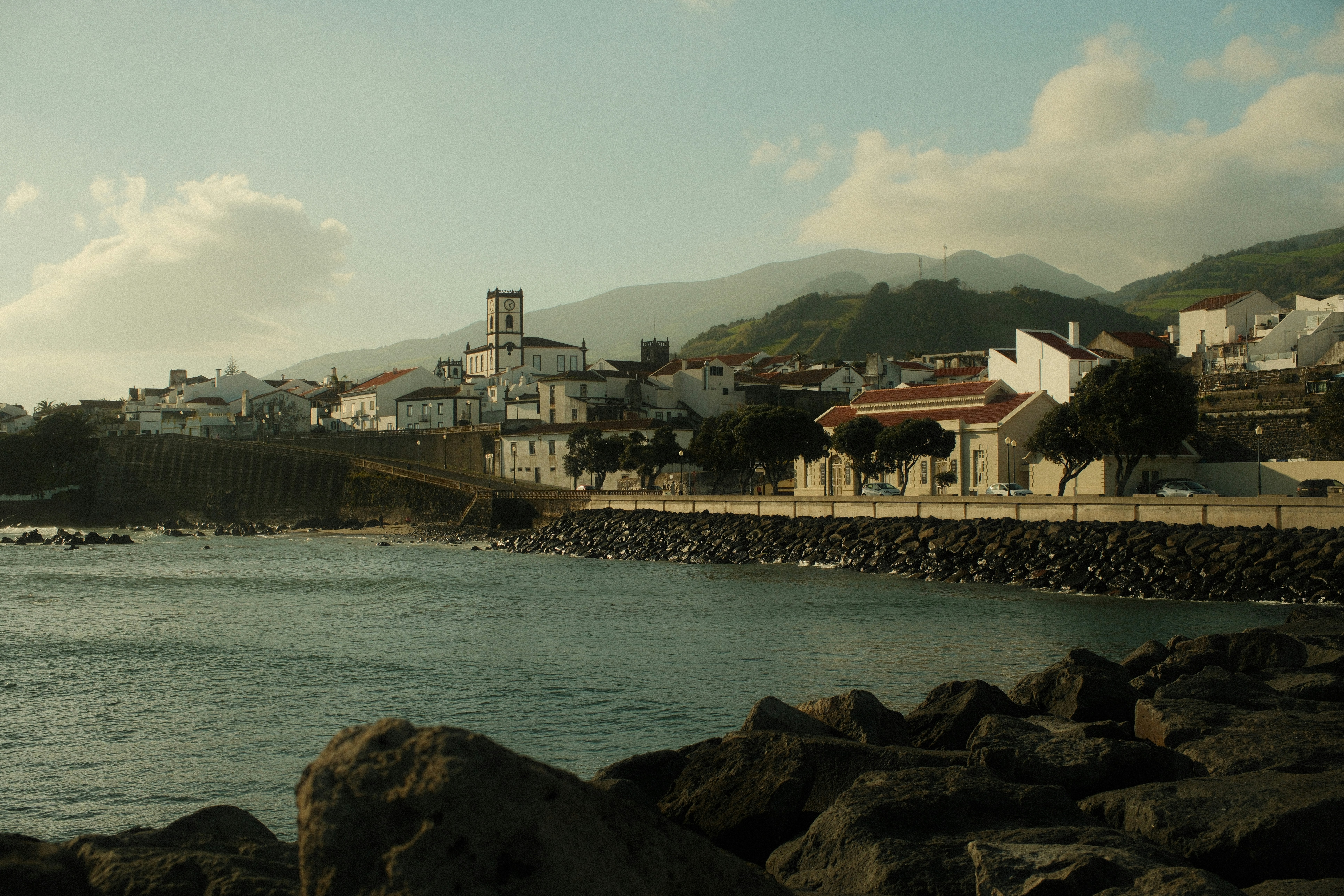 Harbor Line: Sunlit Seaside Town with Rocky Foreground