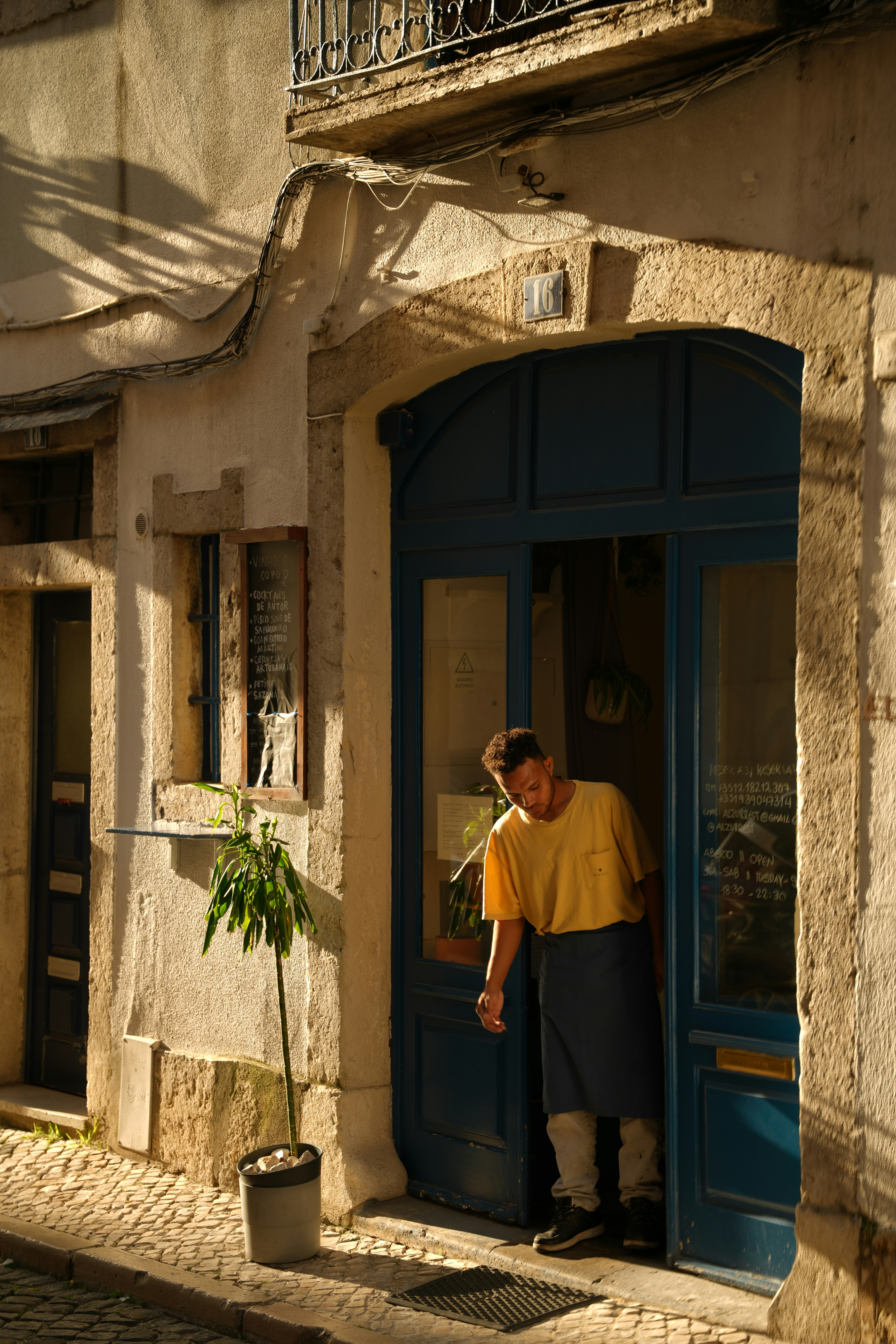 Sunlit doorway: a solitary figure in a mustard shirt steps from a blue frame into the alley light