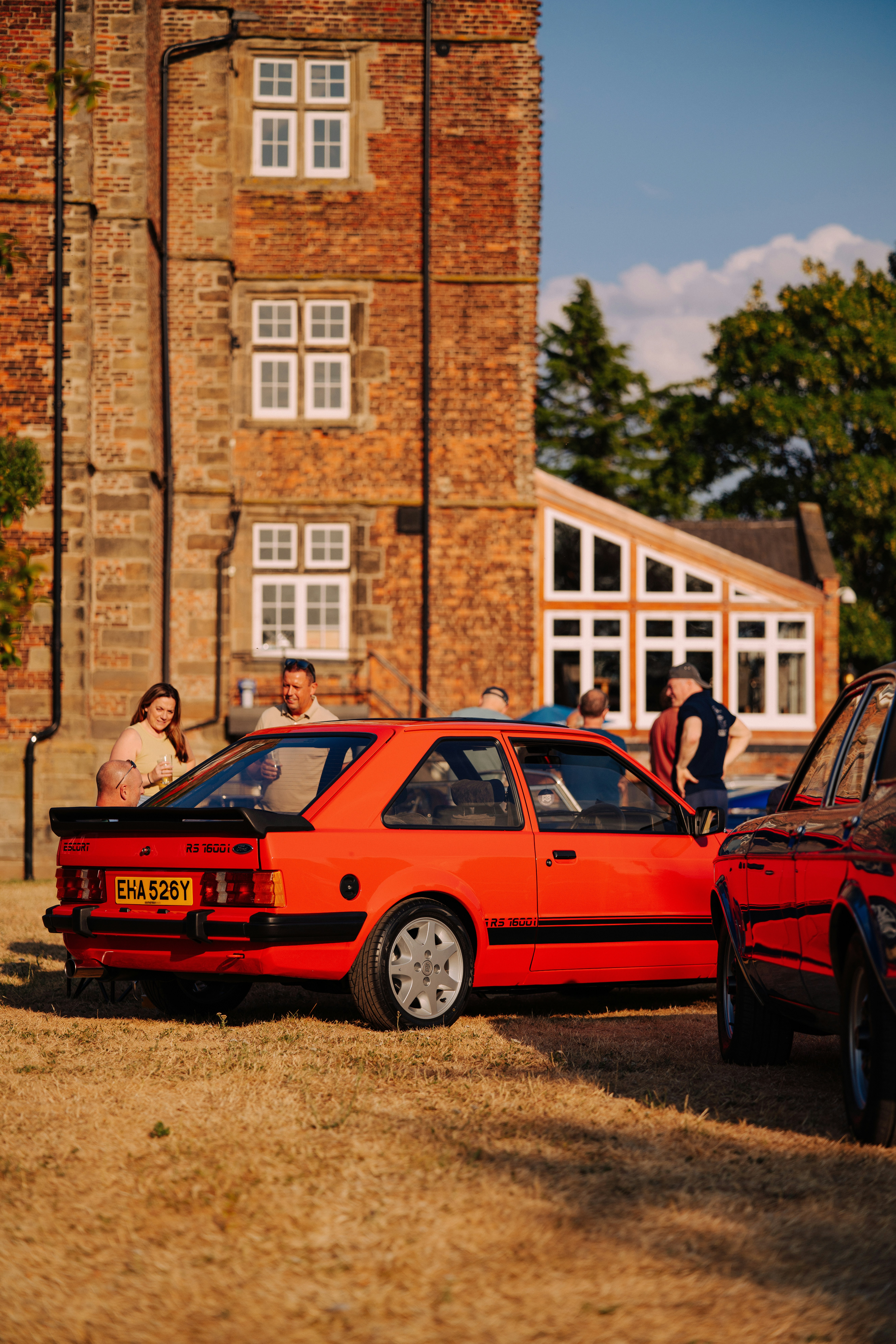 Bright orange car meetup in front of a brick building